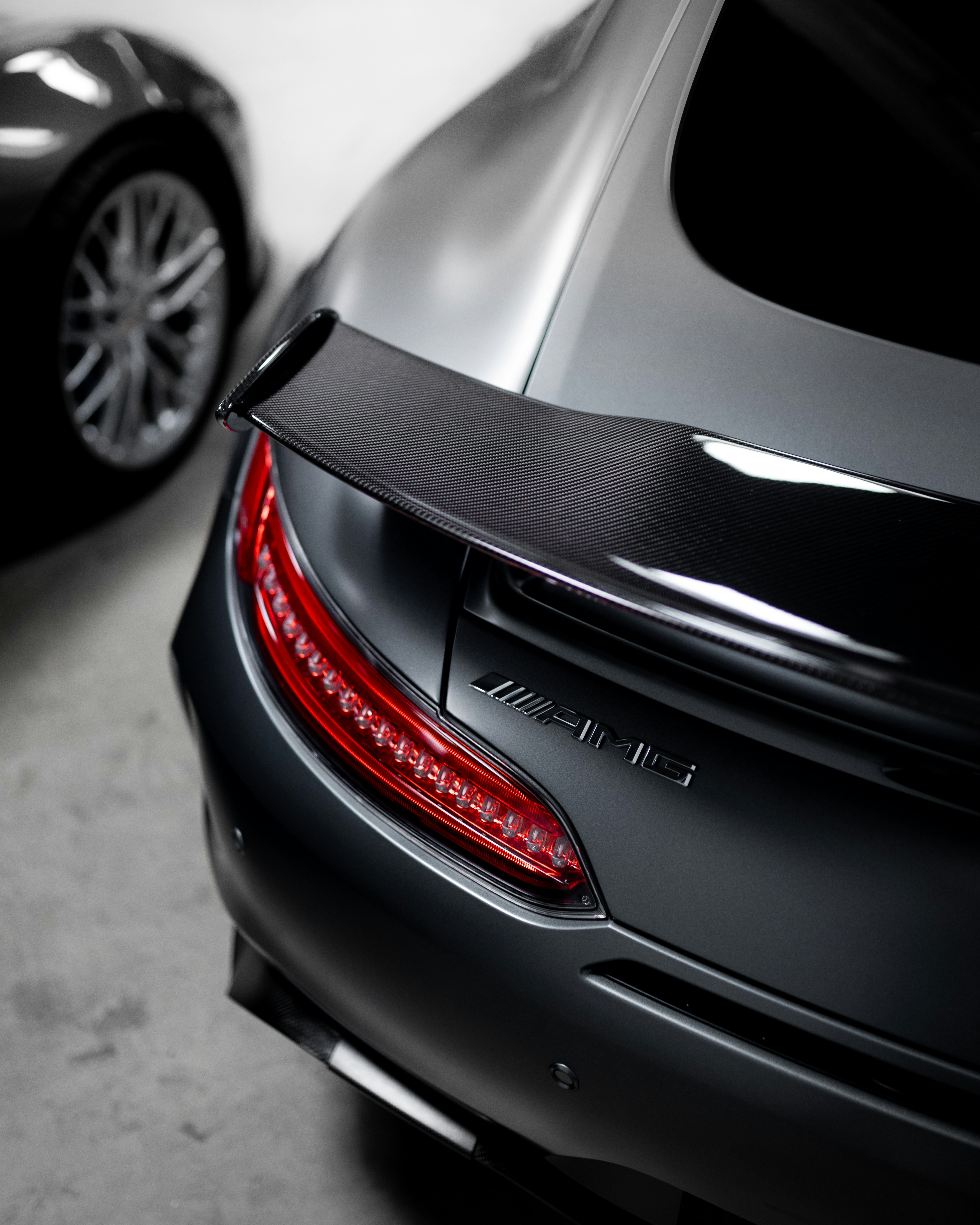 Close-up of a sleek AMG sports car showcasing its aerodynamic rear wing and distinctive taillights in a garage setting.