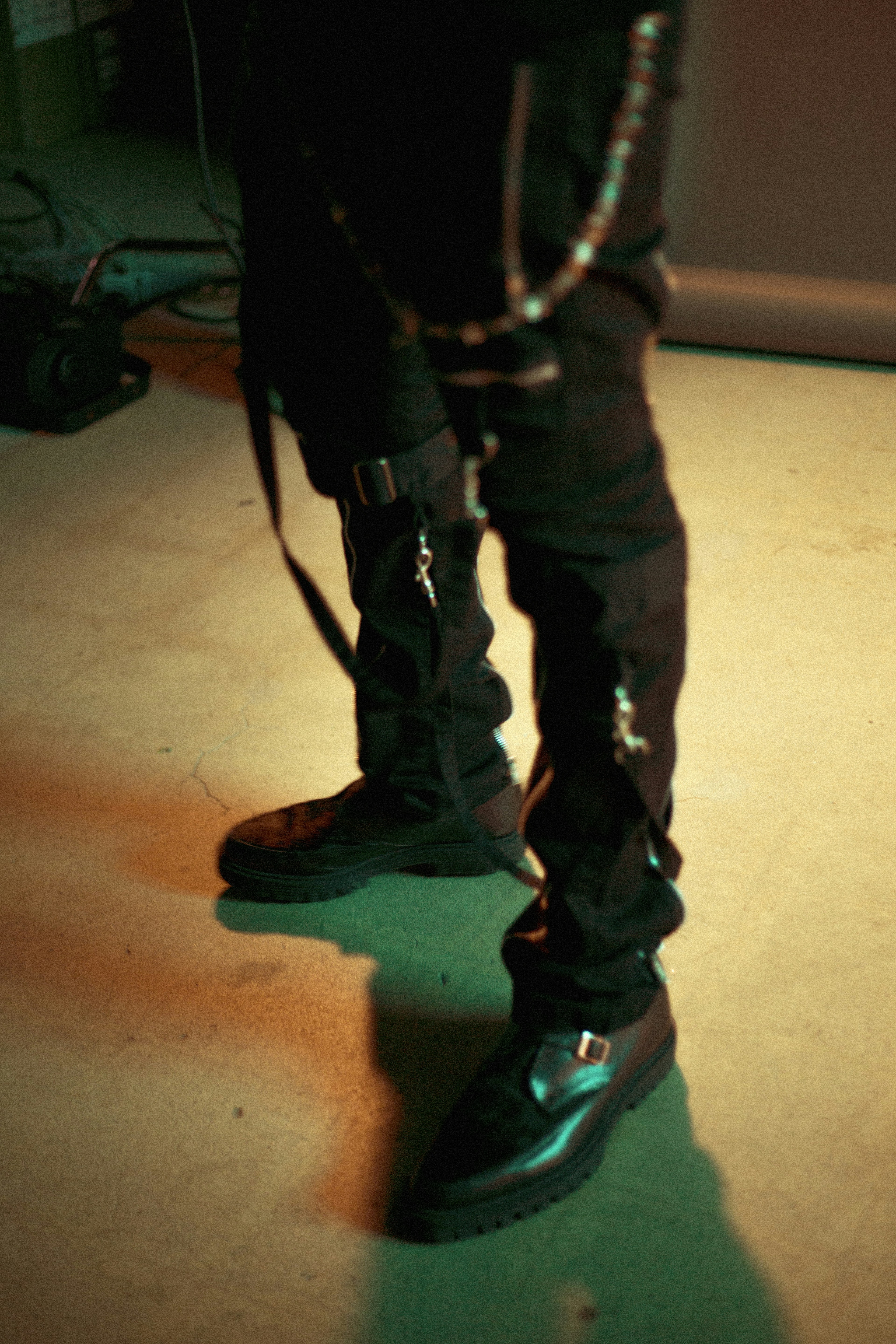Close-up of stylish black footwear and pants, showcasing urban fashion elements against a softly lit background.