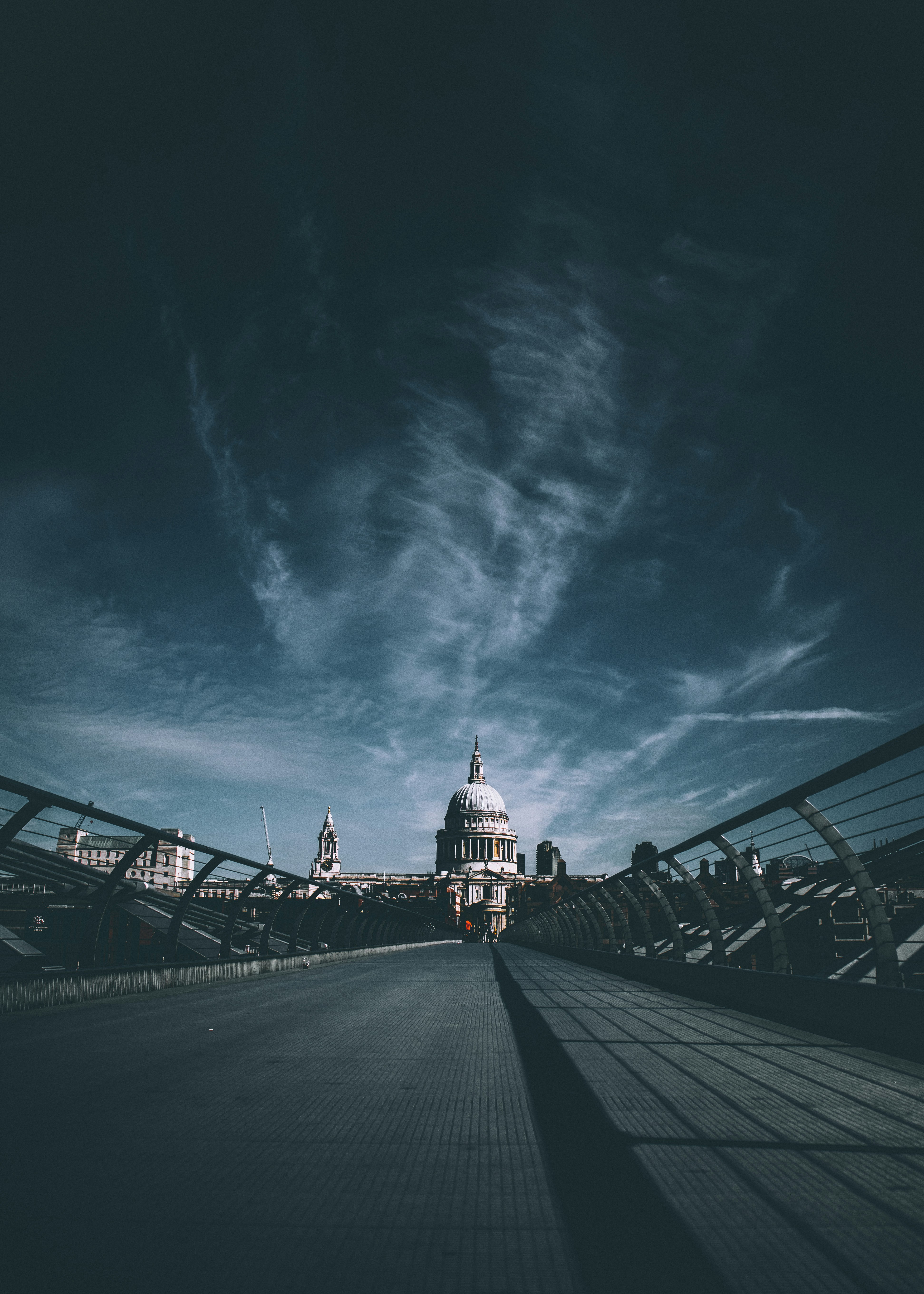 St. Paul's Cathedral towers majestically against a dramatic sky, viewed from a modern pedestrian bridge. The scene captures the contrast between historic architecture and contemporary design.