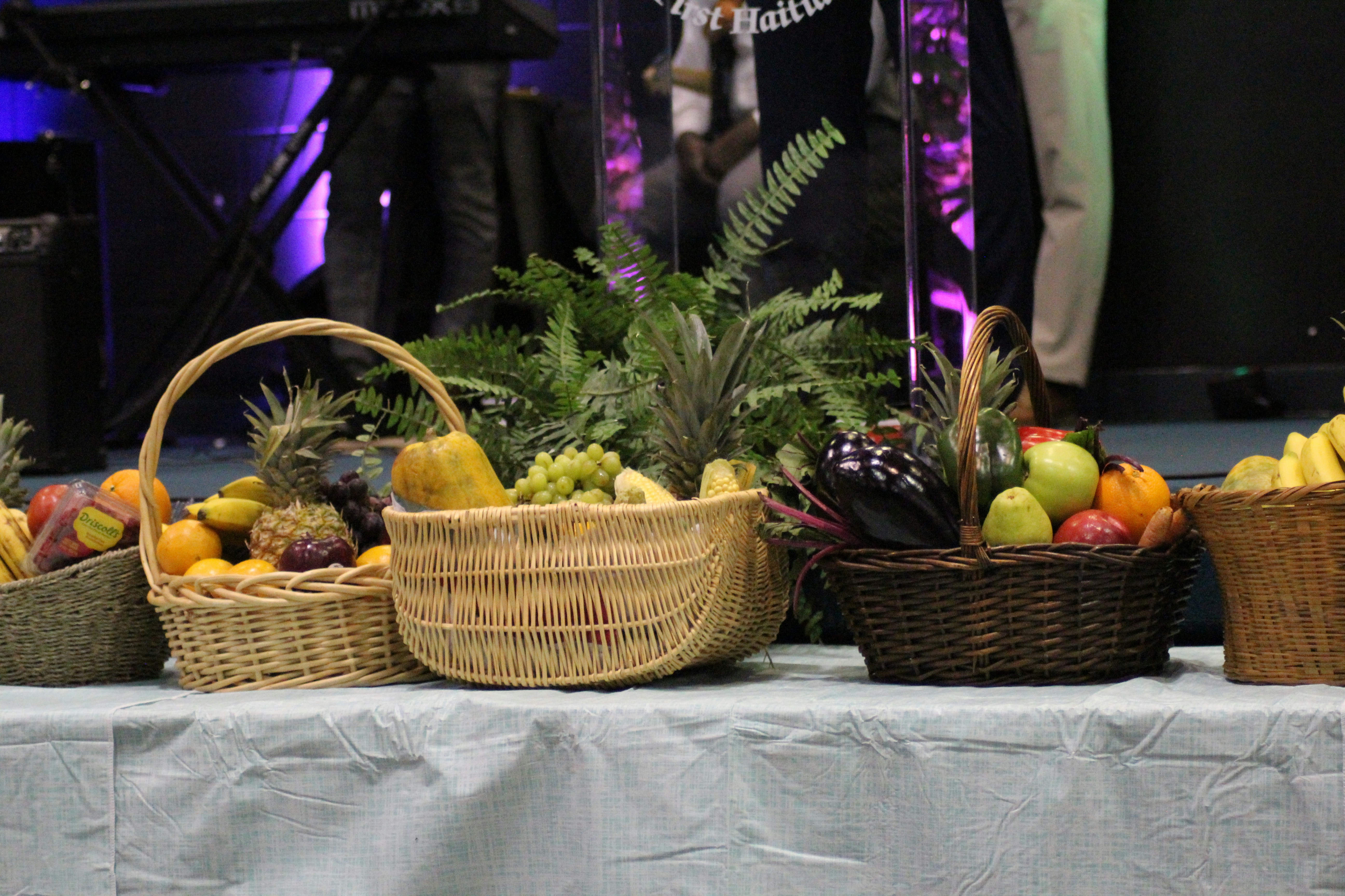 A vibrant display of assorted fruits arranged in woven baskets, showcasing a variety of colors and textures. The setting hints at a communal or celebratory atmosphere.