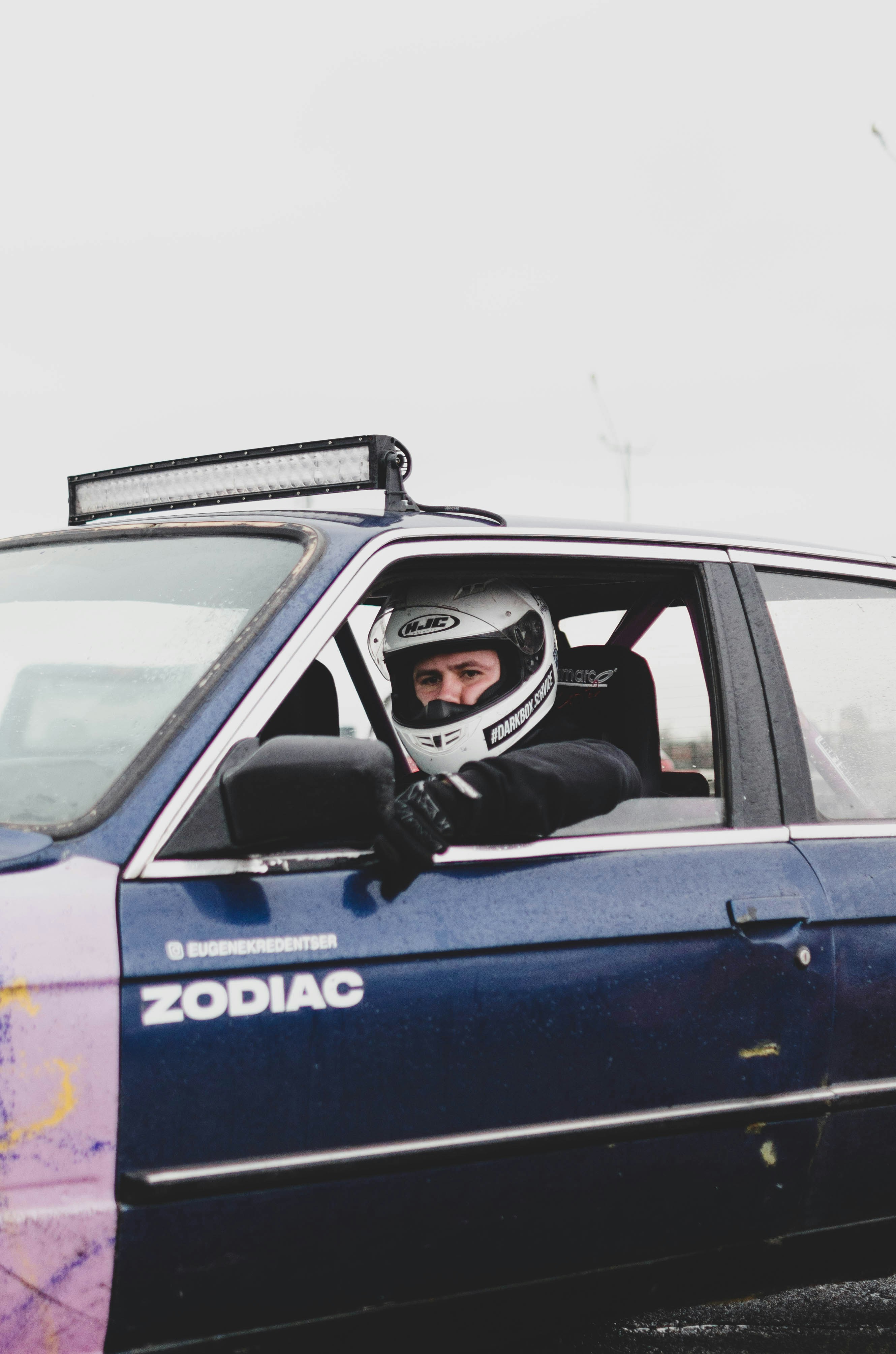 man in black jacket and black pants sitting on blue car