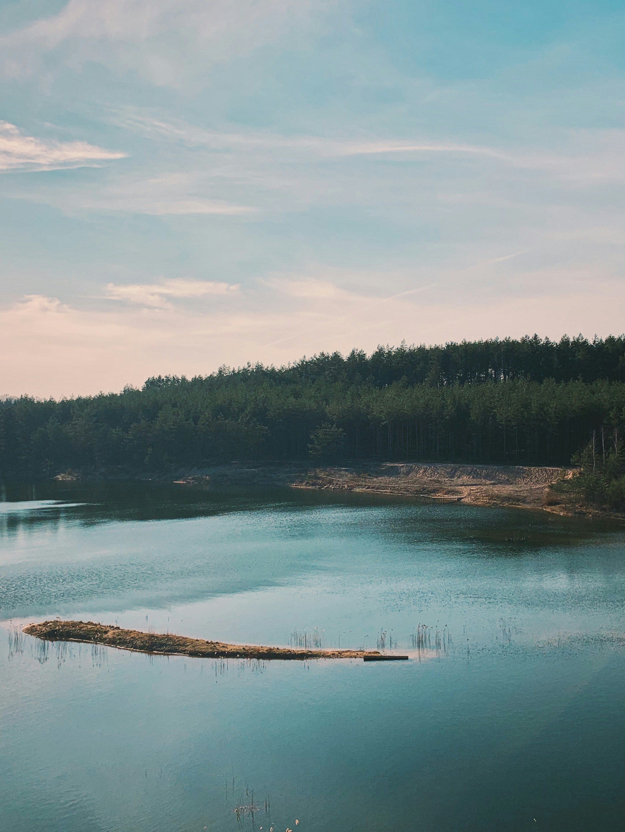 Calm lake reflecting a clear sky and surrounded by lush pine trees, creating a peaceful natural scene.