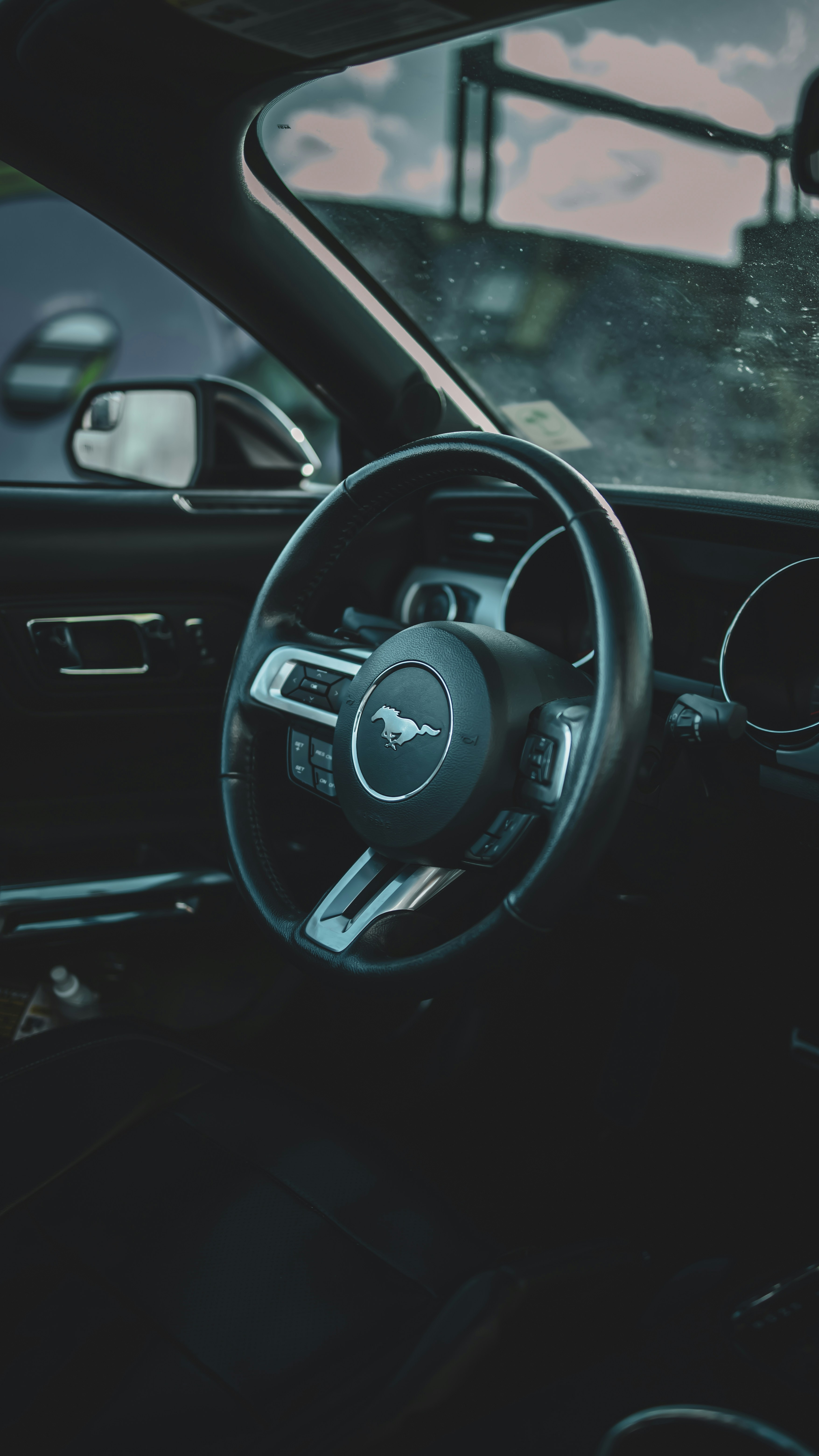 Interior view of a Ford Mustang's steering wheel and dashboard, showcasing the iconic logo and modern design elements.