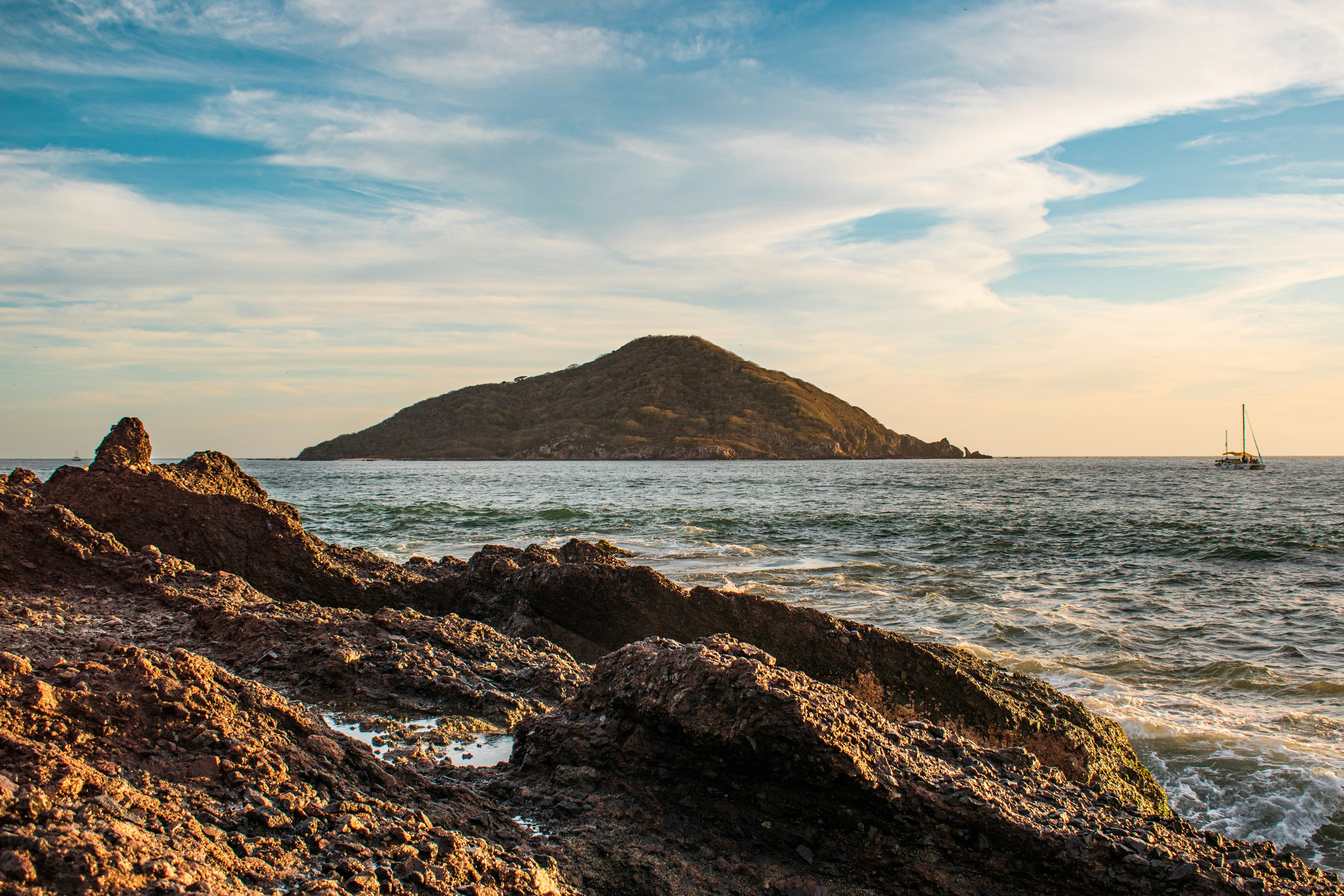Rocky shoreline with a distant island under a vibrant evening sky.