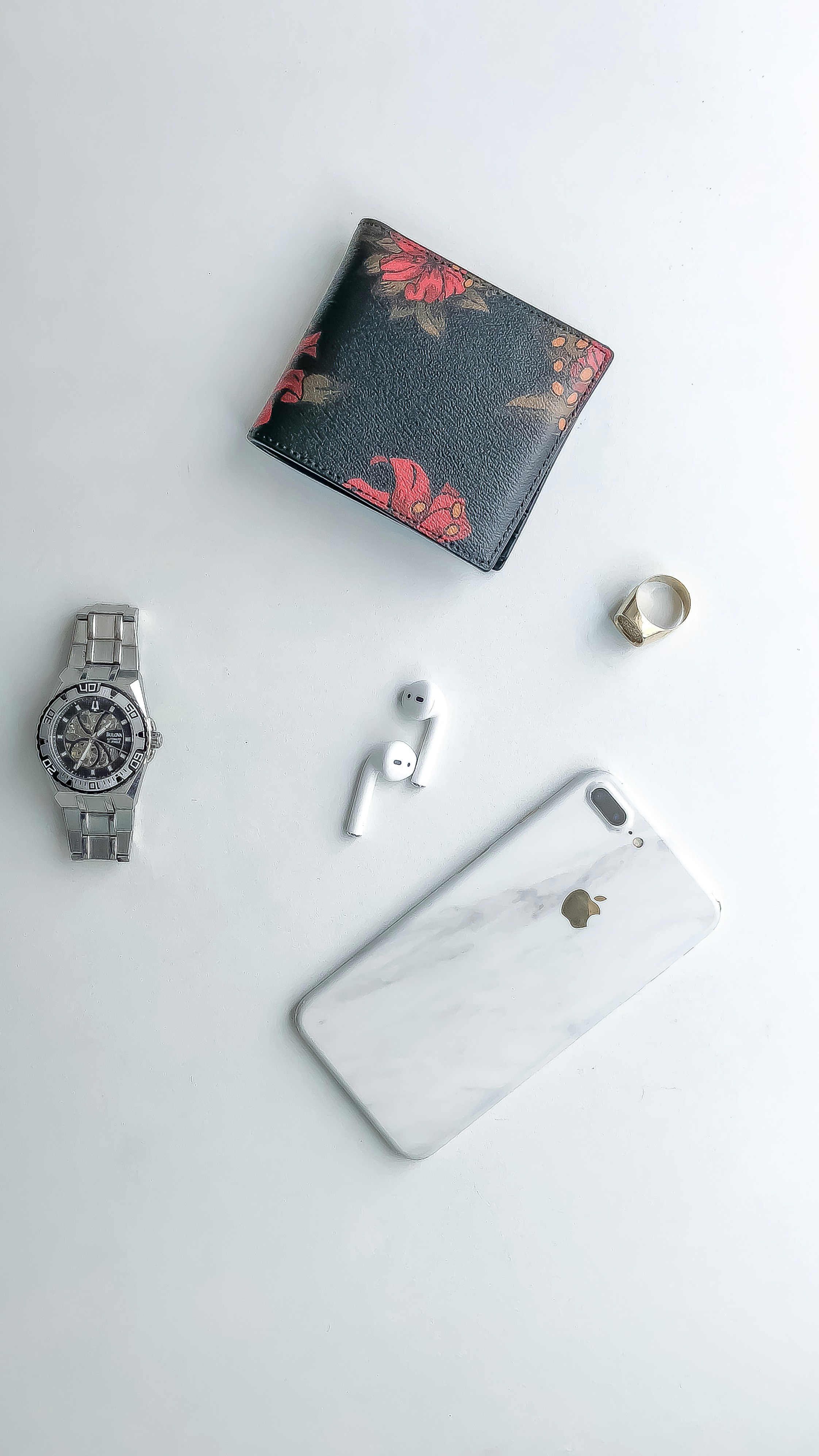 Minimalist desk flat lay: metallic watch, marble iPhone, and floral wallet