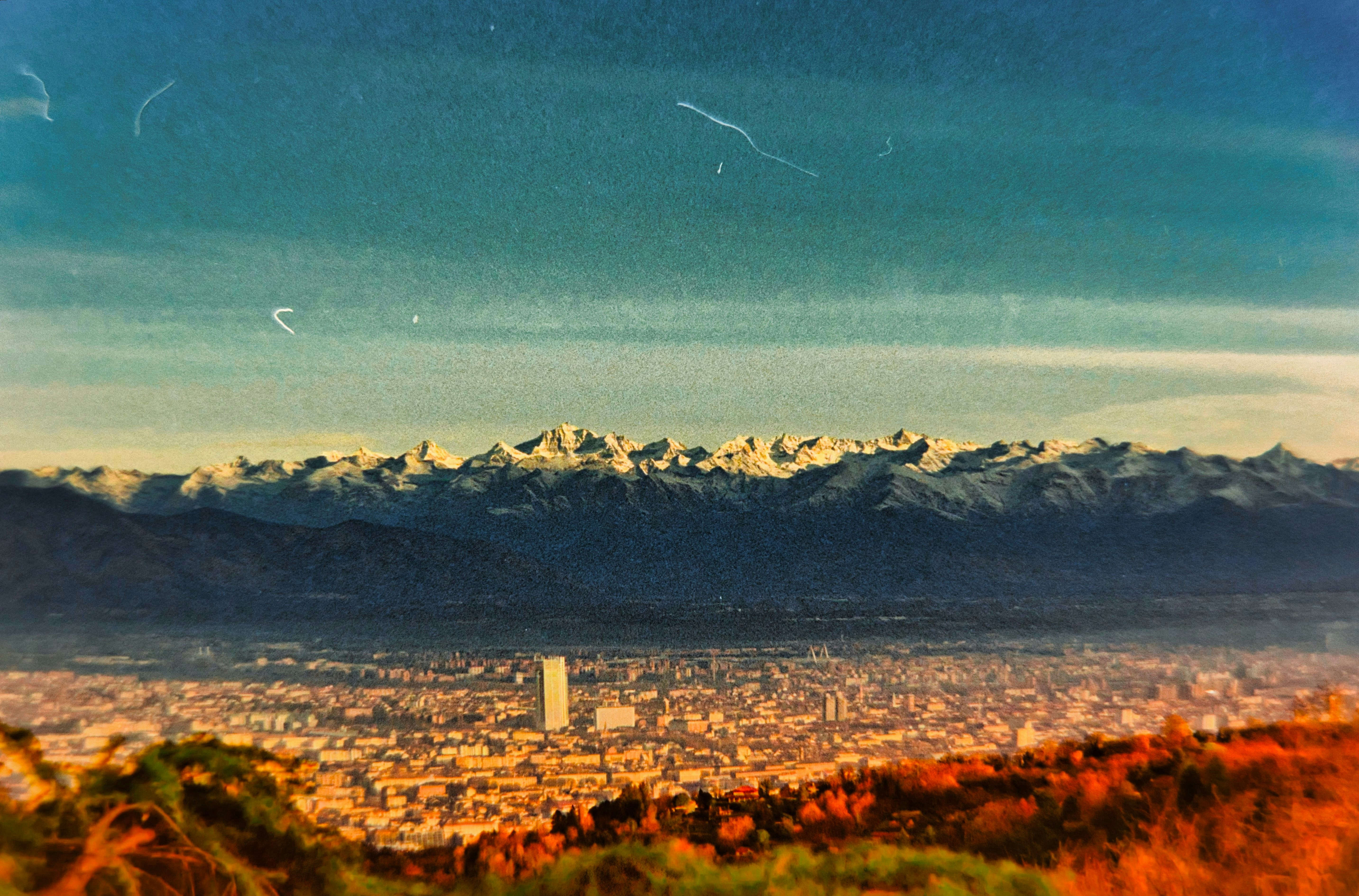 Cityscape with a distant range of snow-covered mountains under a clear sky.