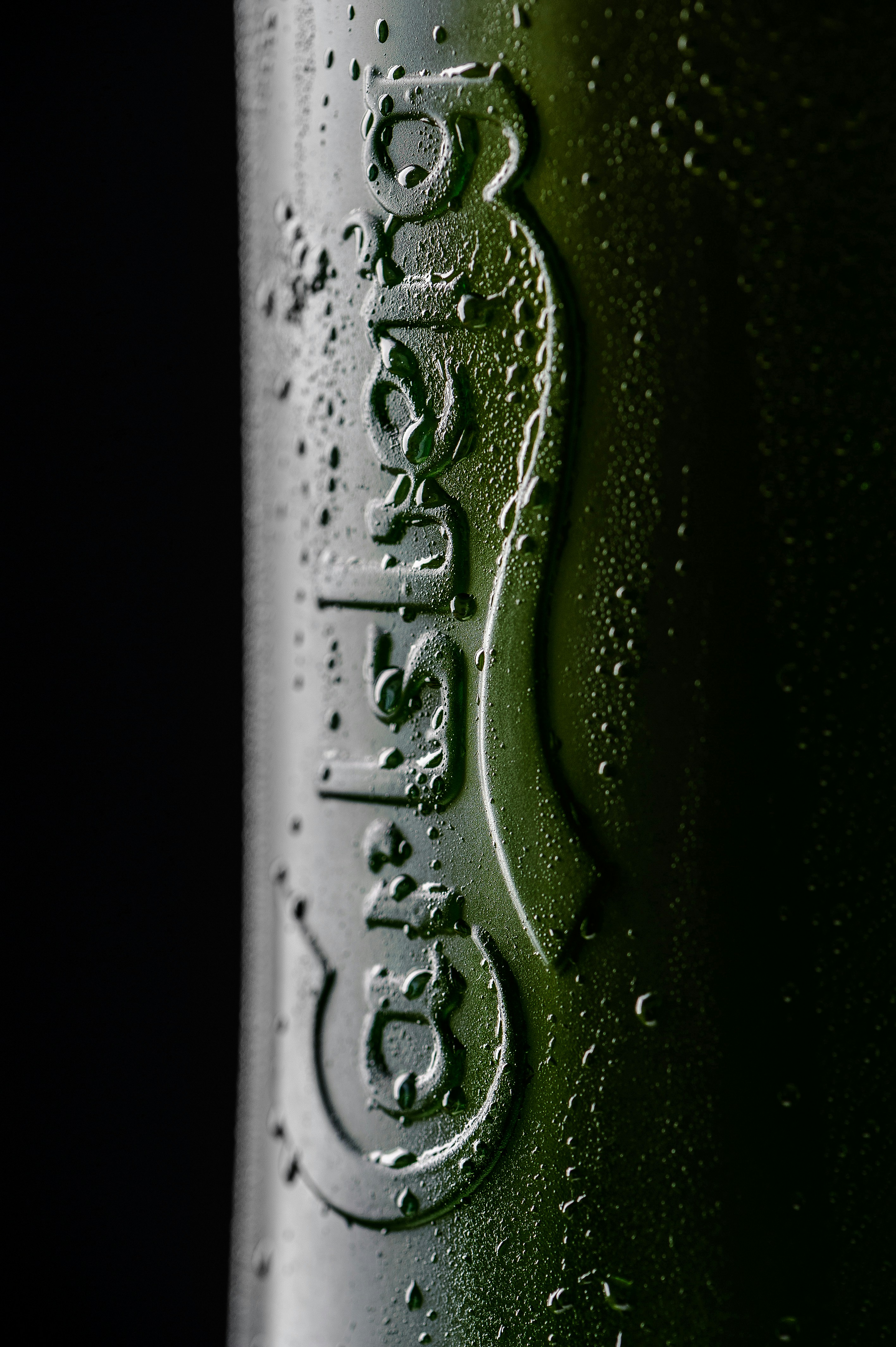 Close-up view of a Carlsberg beer bottle showcasing condensation and embossed logo against a dark background.