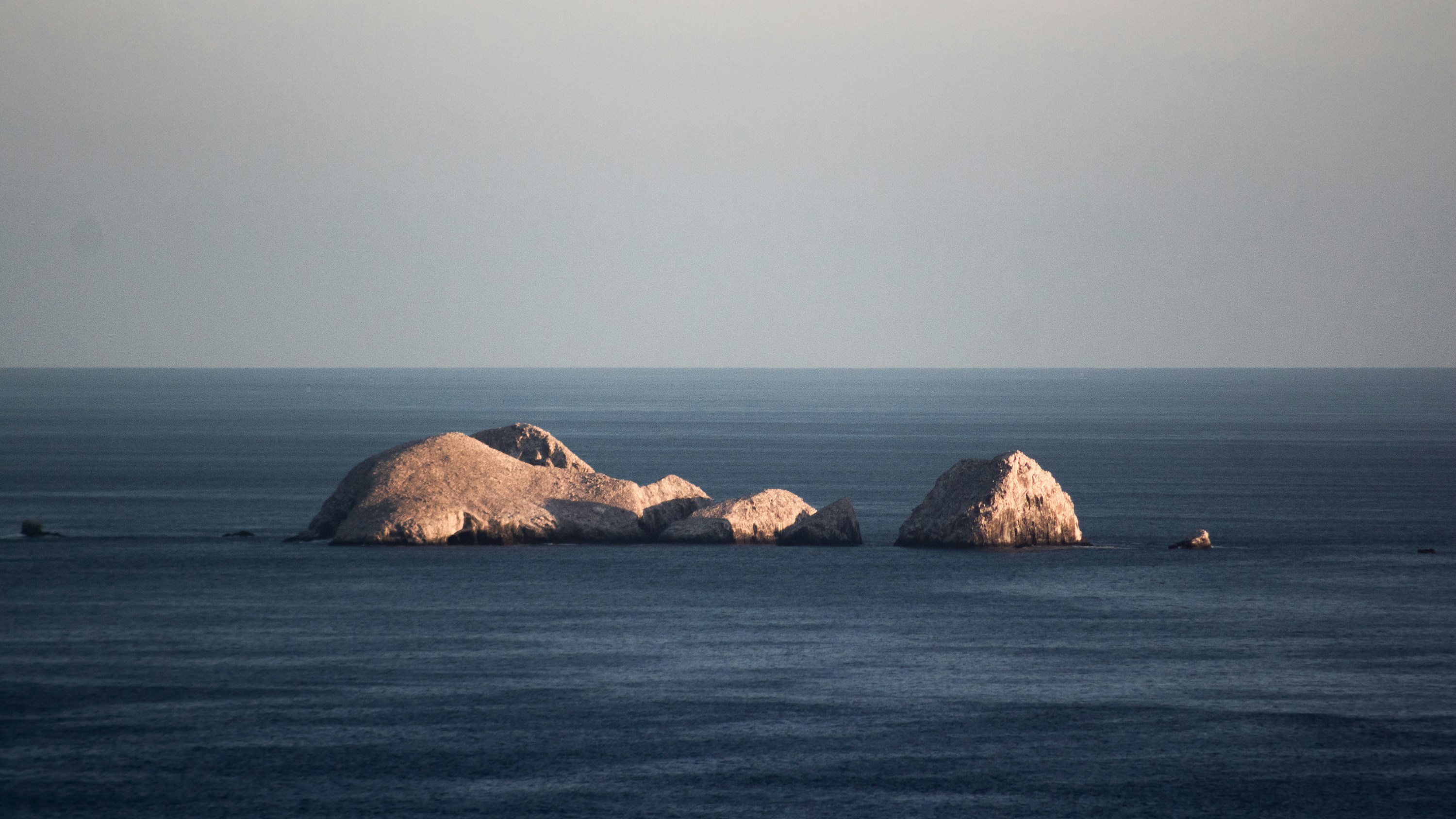 Distant rocky islands emerge from the calm blue sea under a soft, pale sky.