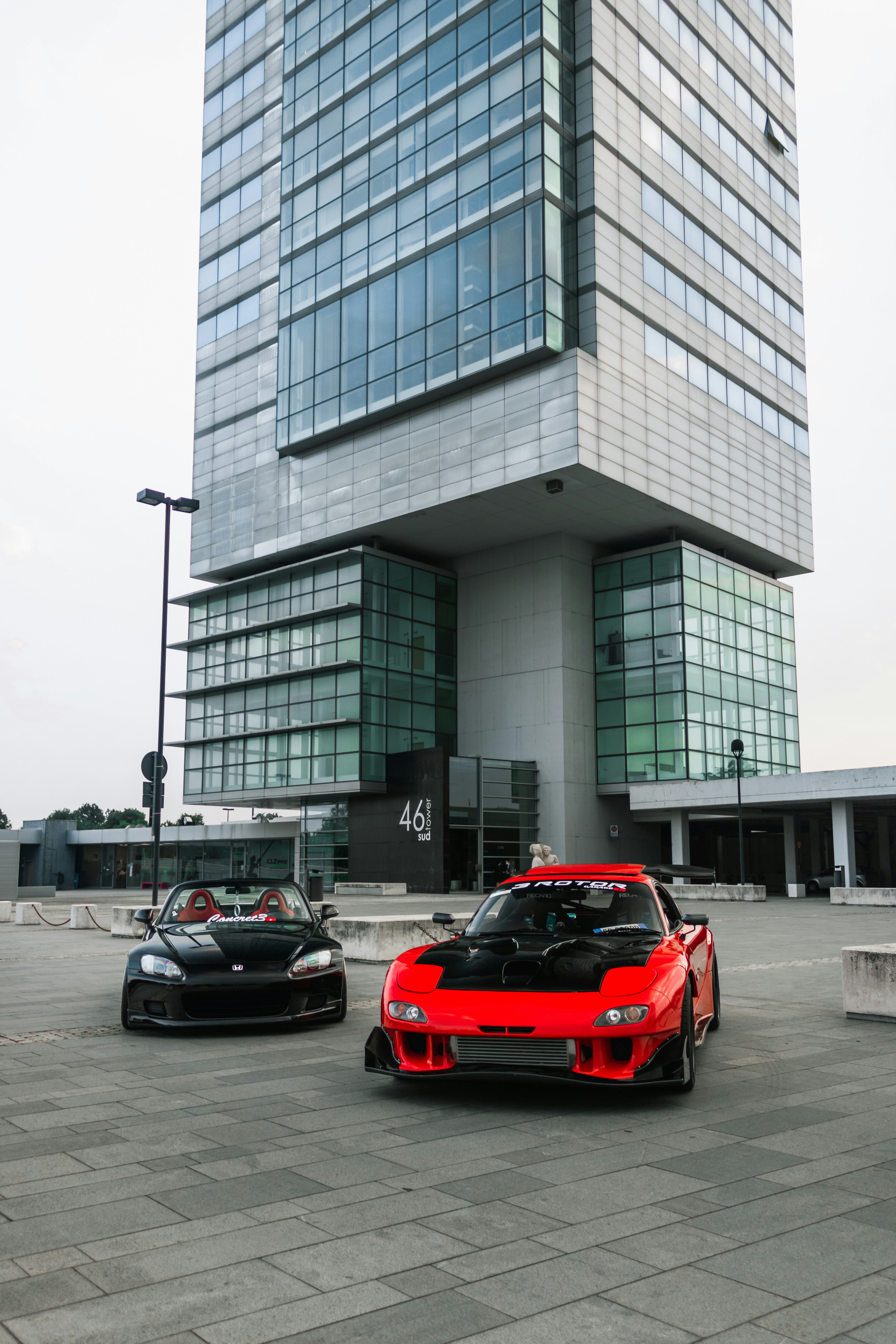 Red and black sports cars parked beside a modern high-rise building during the day.