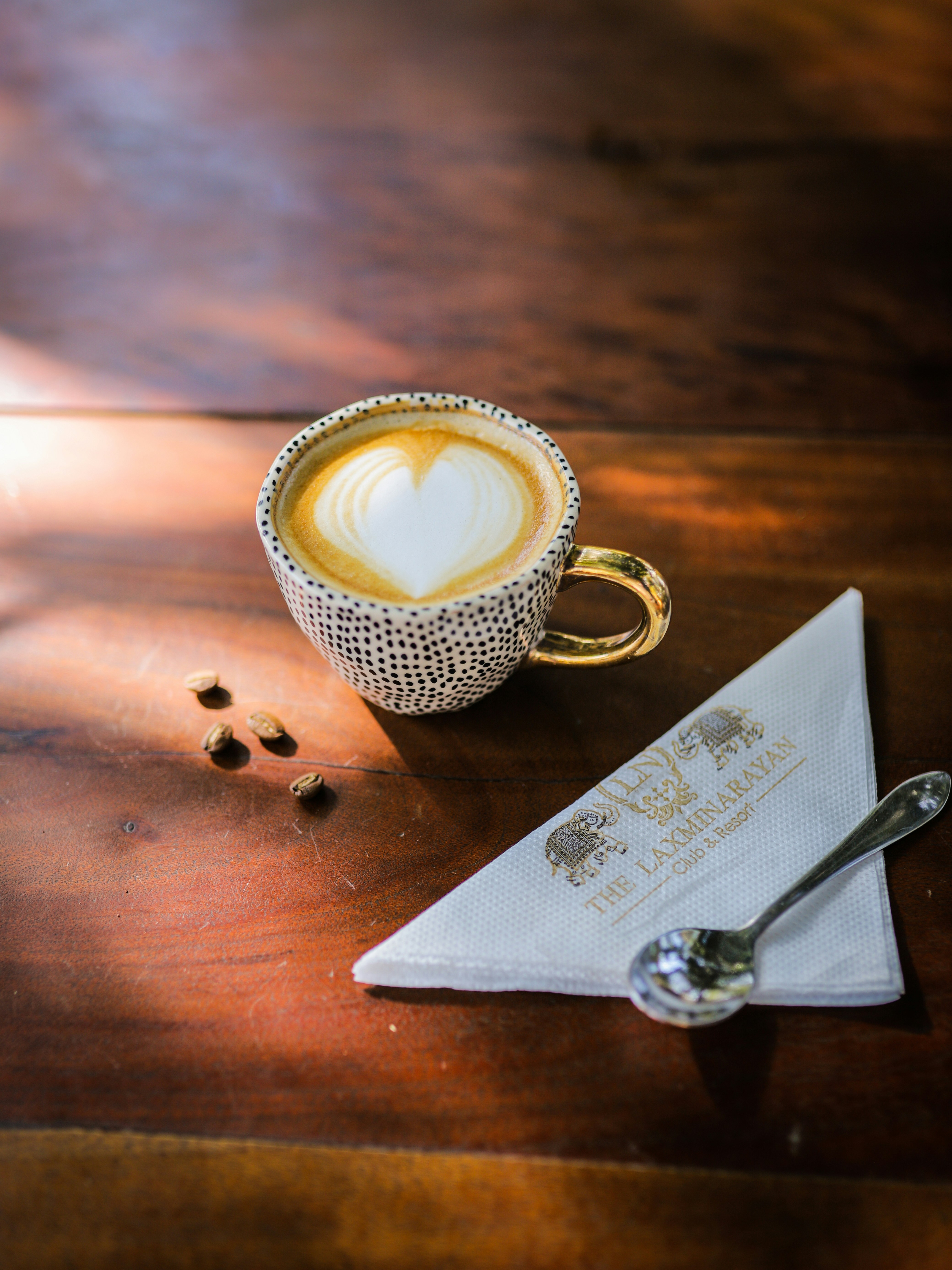 Artfully crafted latte with a heart design, accompanied by coffee beans and a neatly folded napkin on a wooden table.