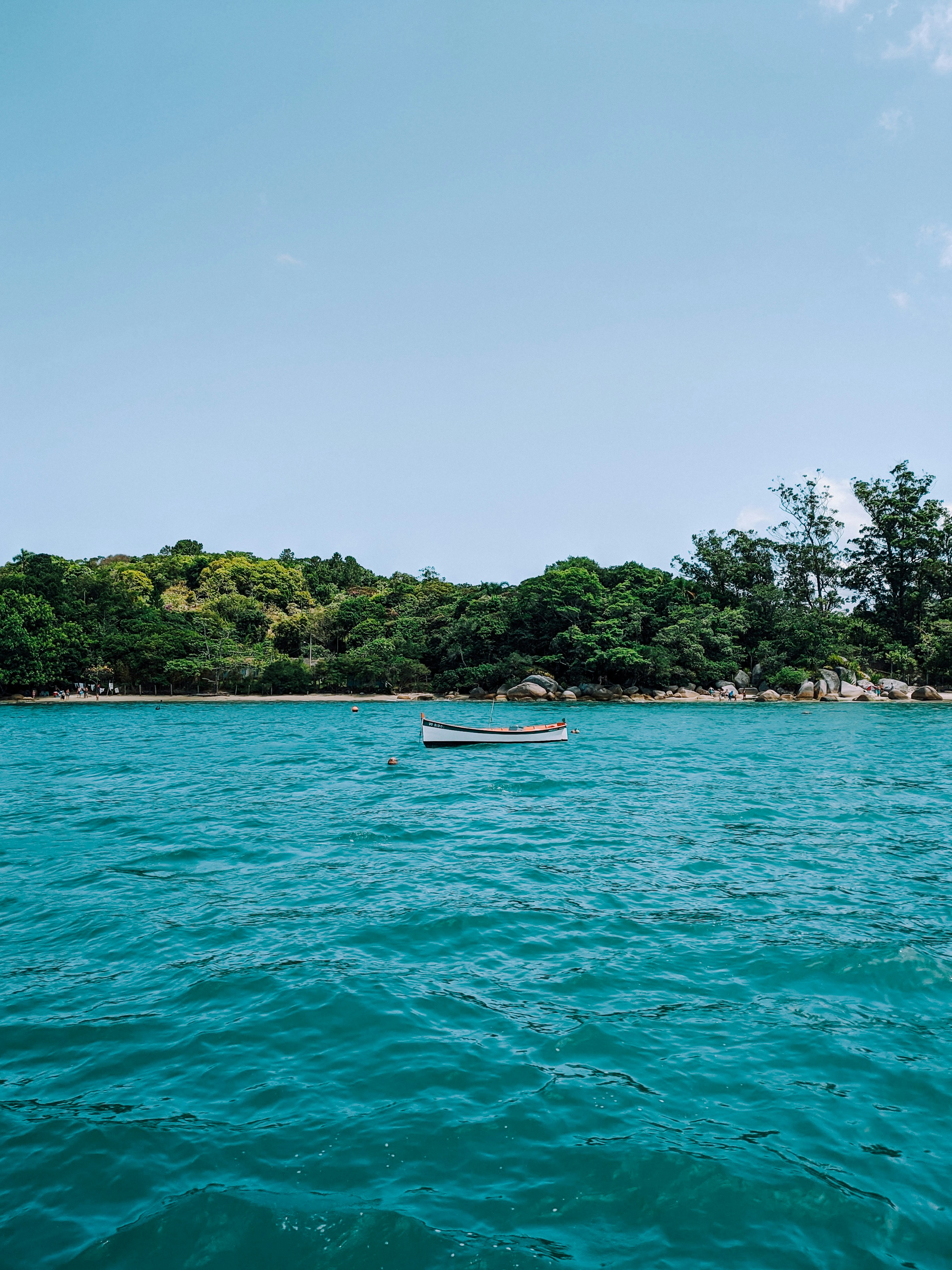 Lone boat gently floating in turquoise waters with lush greenery lining the shore.