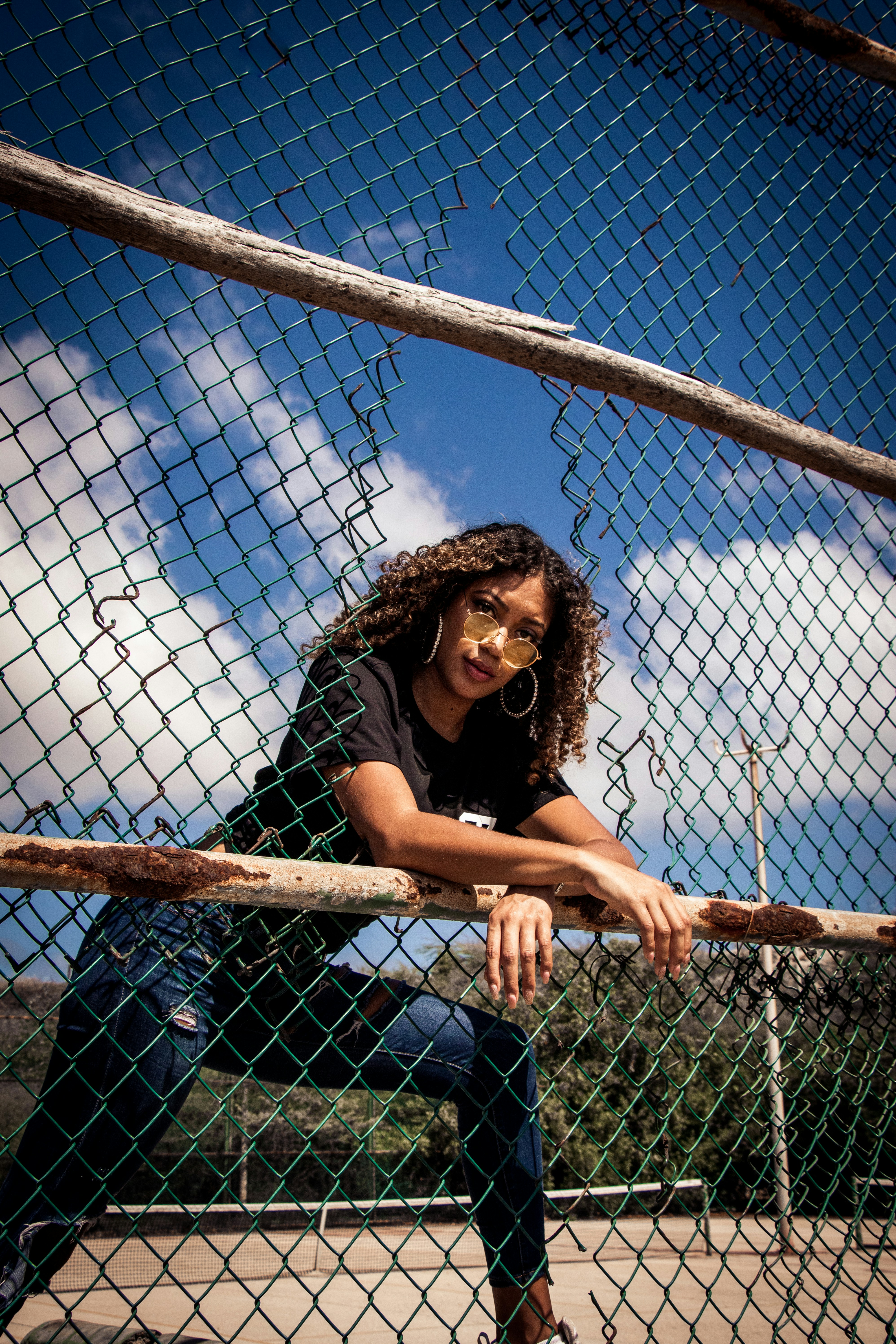 Through the Mesh: A Portrait Framed by Weathered Chain-Link Against a Blue Sky