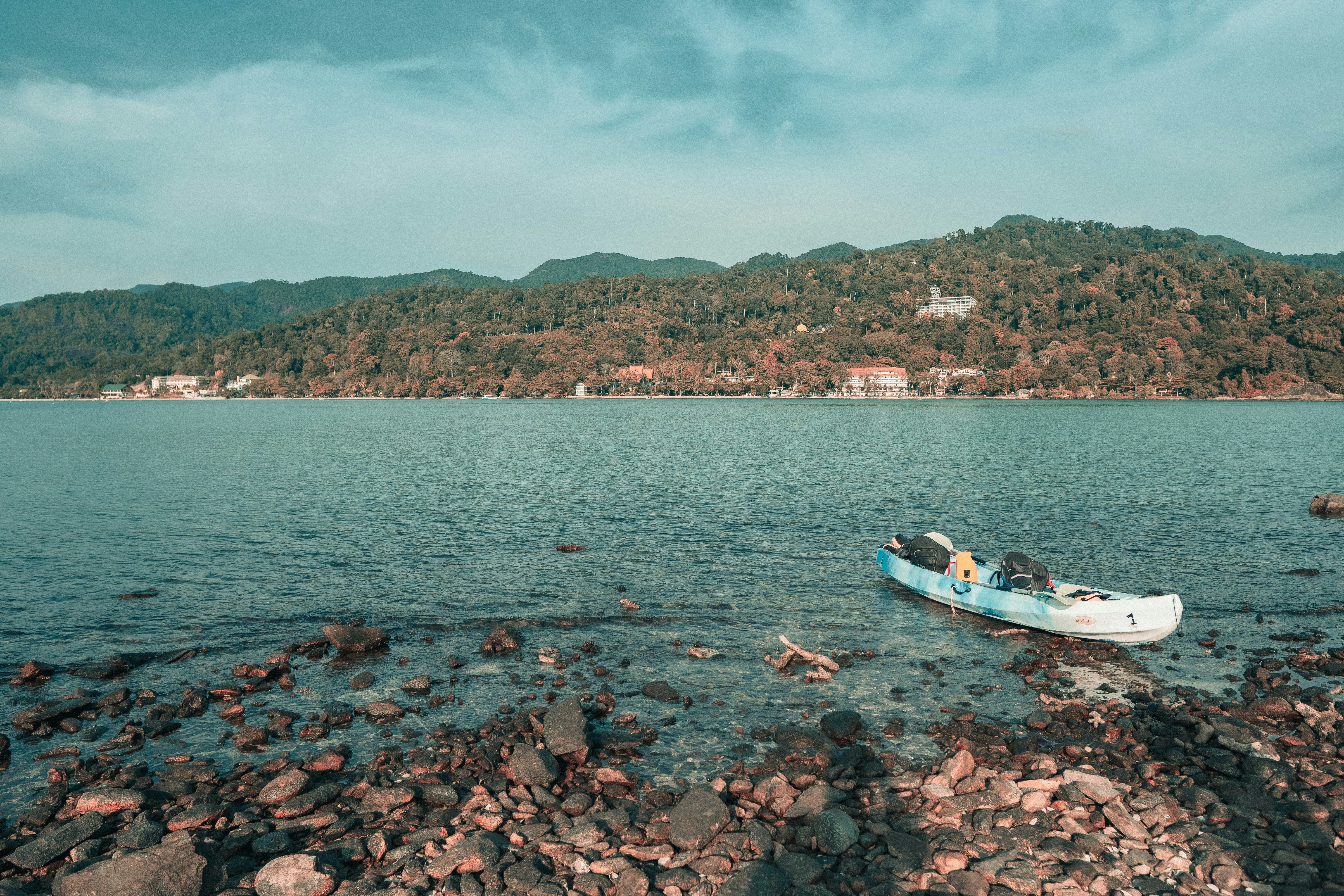 A Lone Boat Resting Along a Rocky Shoreline Under Quiet Coastal Hills