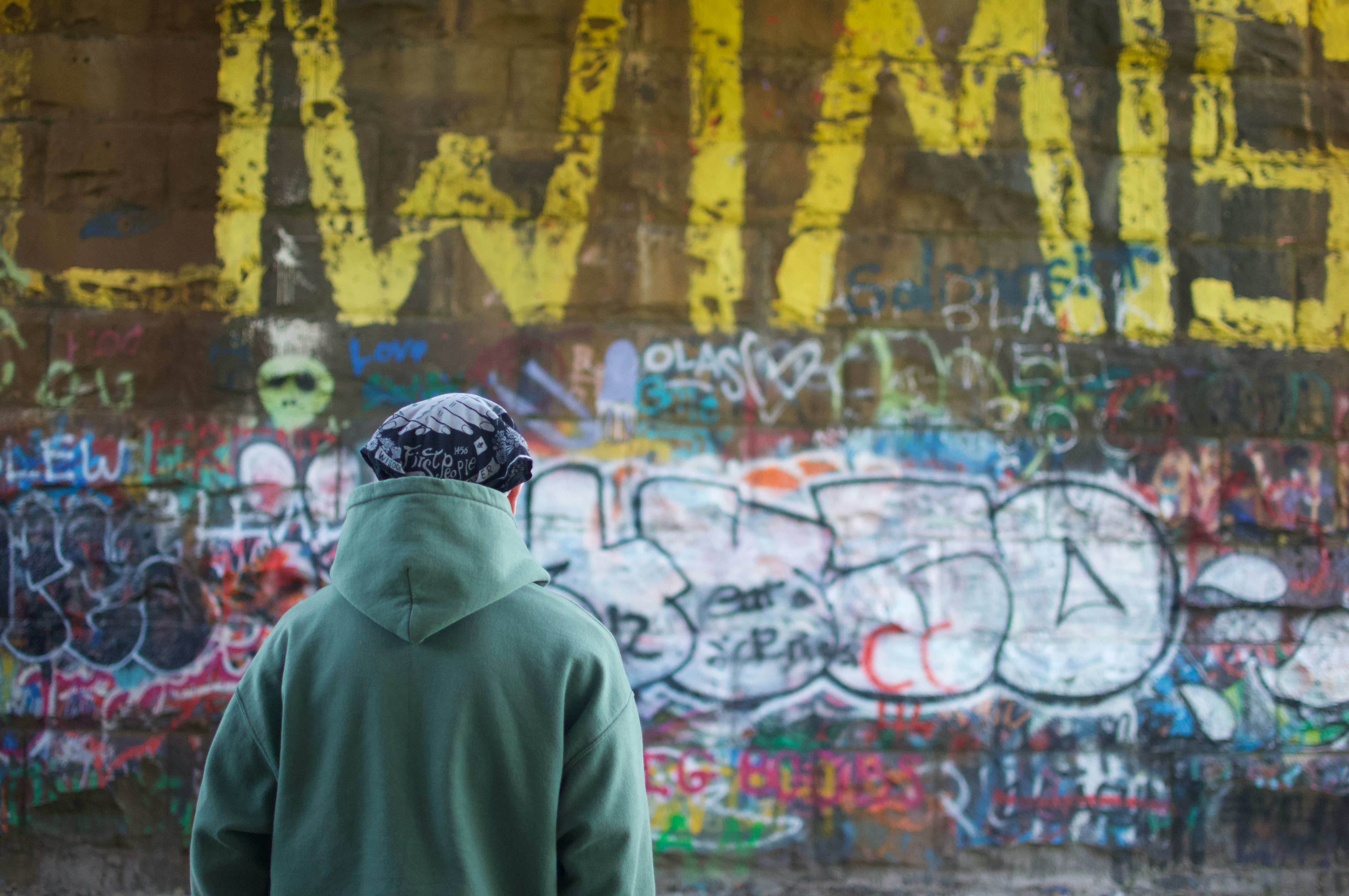Individual standing before a vibrant graffiti-covered wall, immersed in the urban art scene. The backdrop features bold lettering and colorful tags.