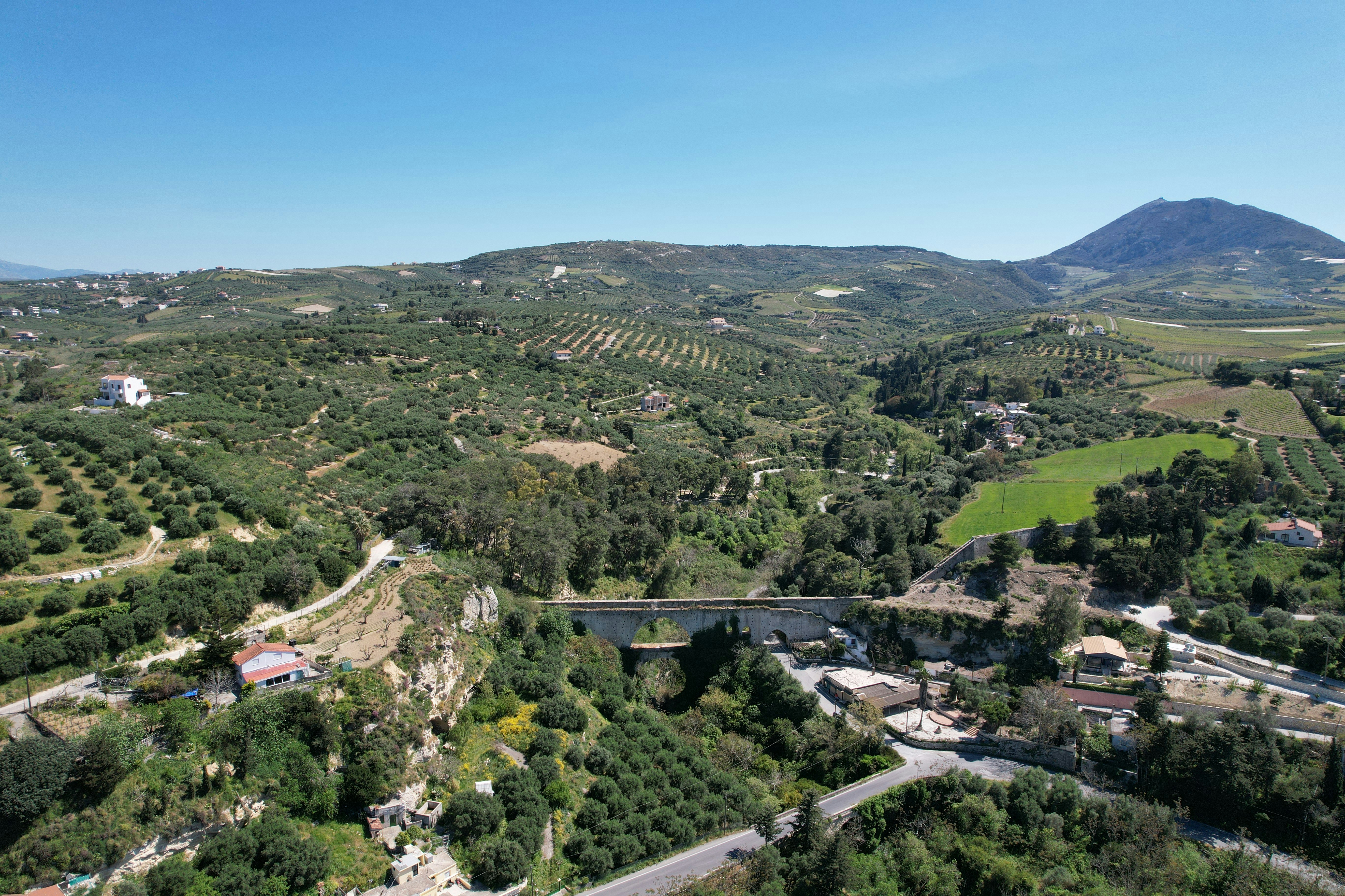 Aerial view showcasing lush green valleys, terraced orchards, and a historic stone bridge nestled in the landscape.