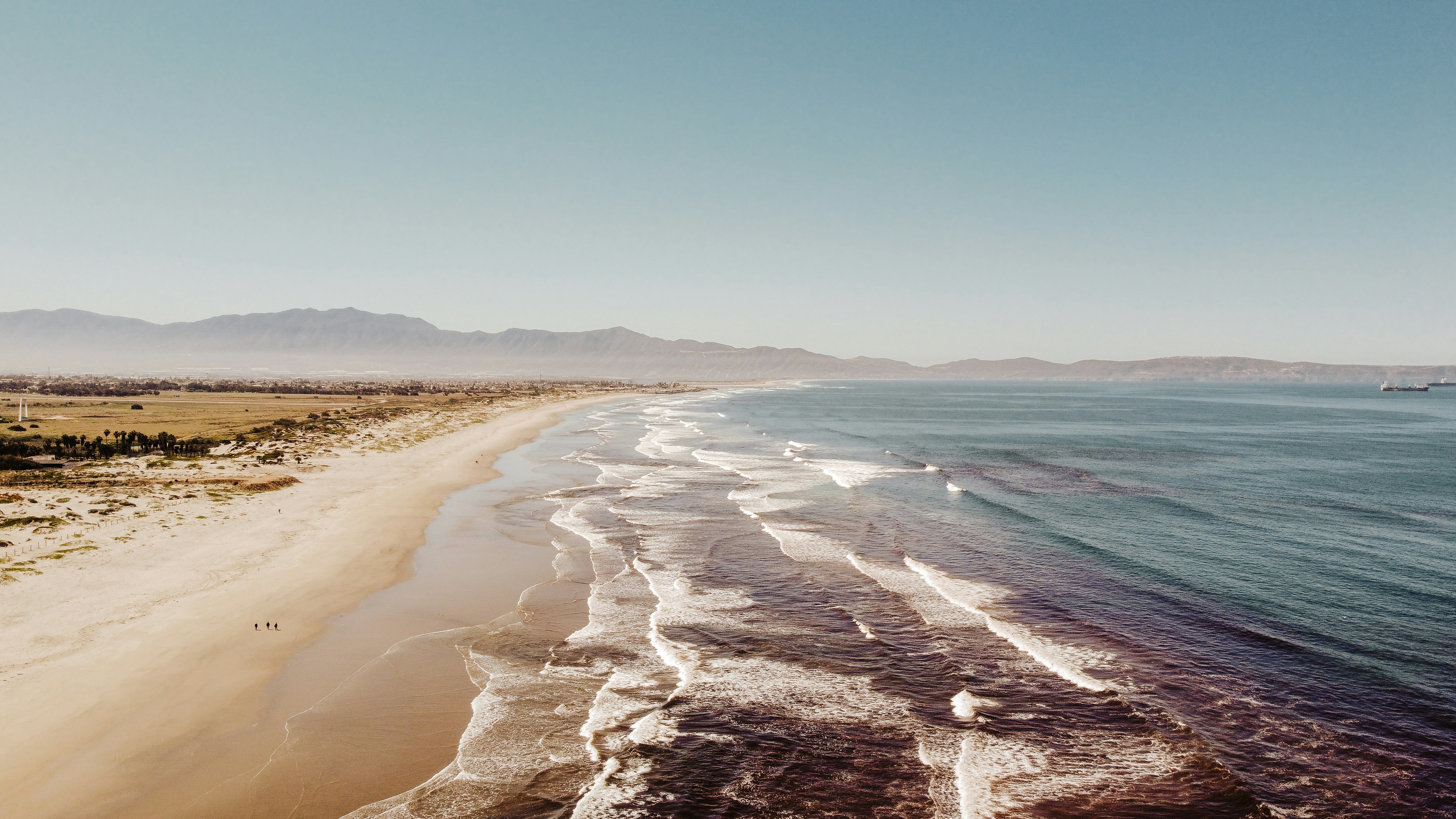 Expansive beach meeting gentle ocean waves under a clear blue sky.
