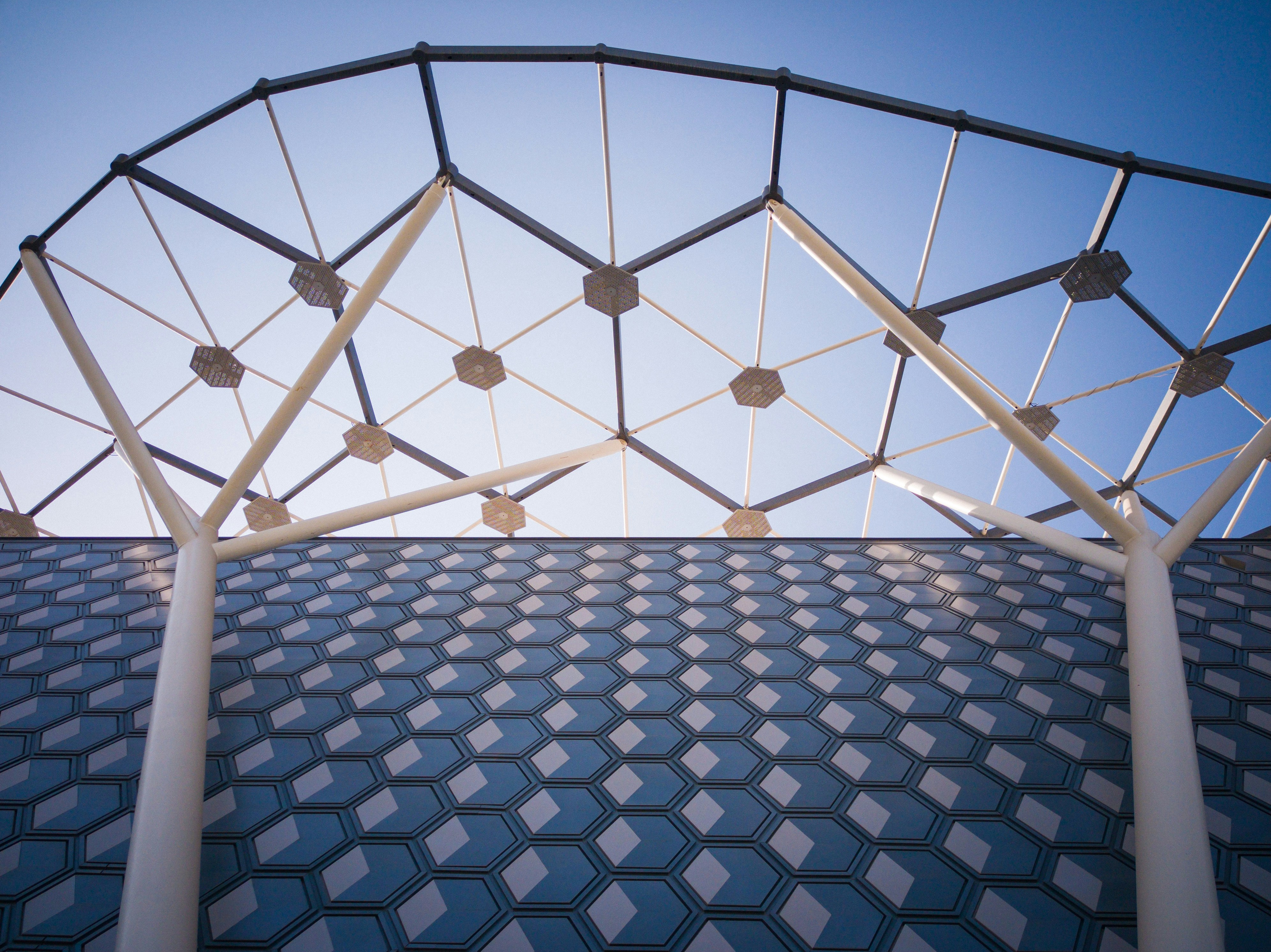 Intricate architectural design featuring a hexagonal facade and a modern canopy structure against a clear blue sky.