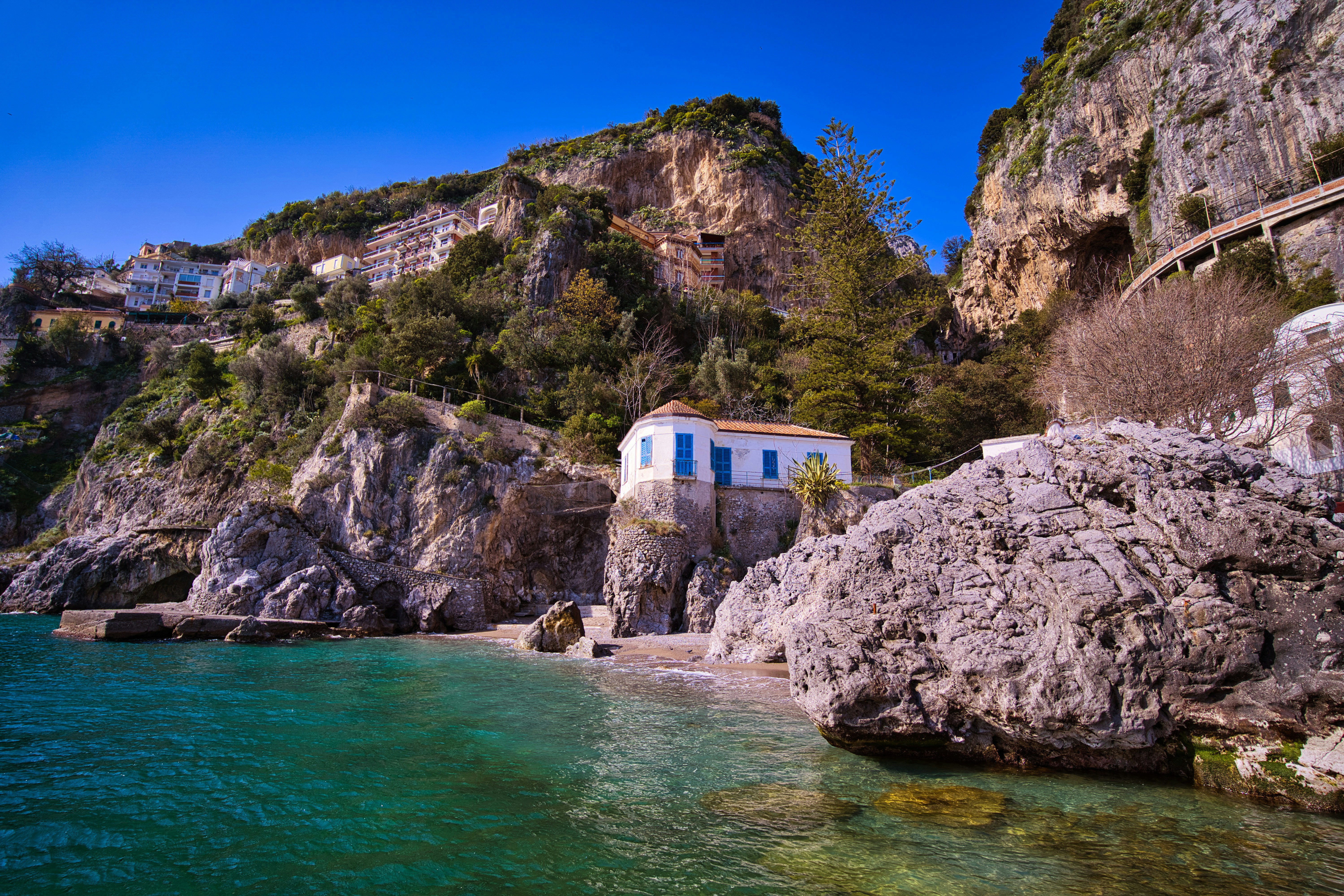 Charming white cottage nestled between rugged cliffs and clear turquoise waters, showcasing a serene coastal landscape.