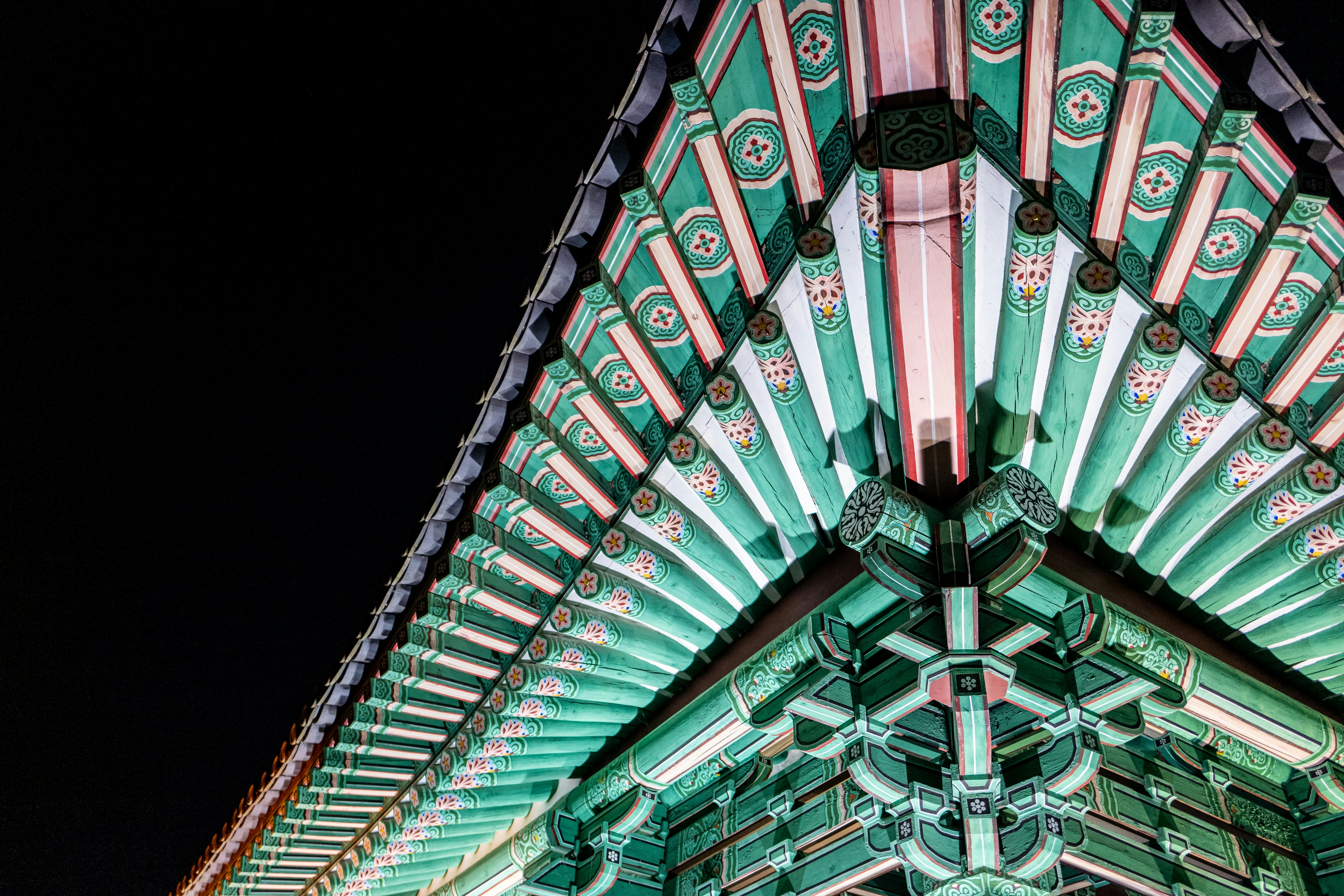 Vibrant traditional eaves adorned with intricate patterns, illuminated against the night sky. The architectural beauty showcases cultural heritage.