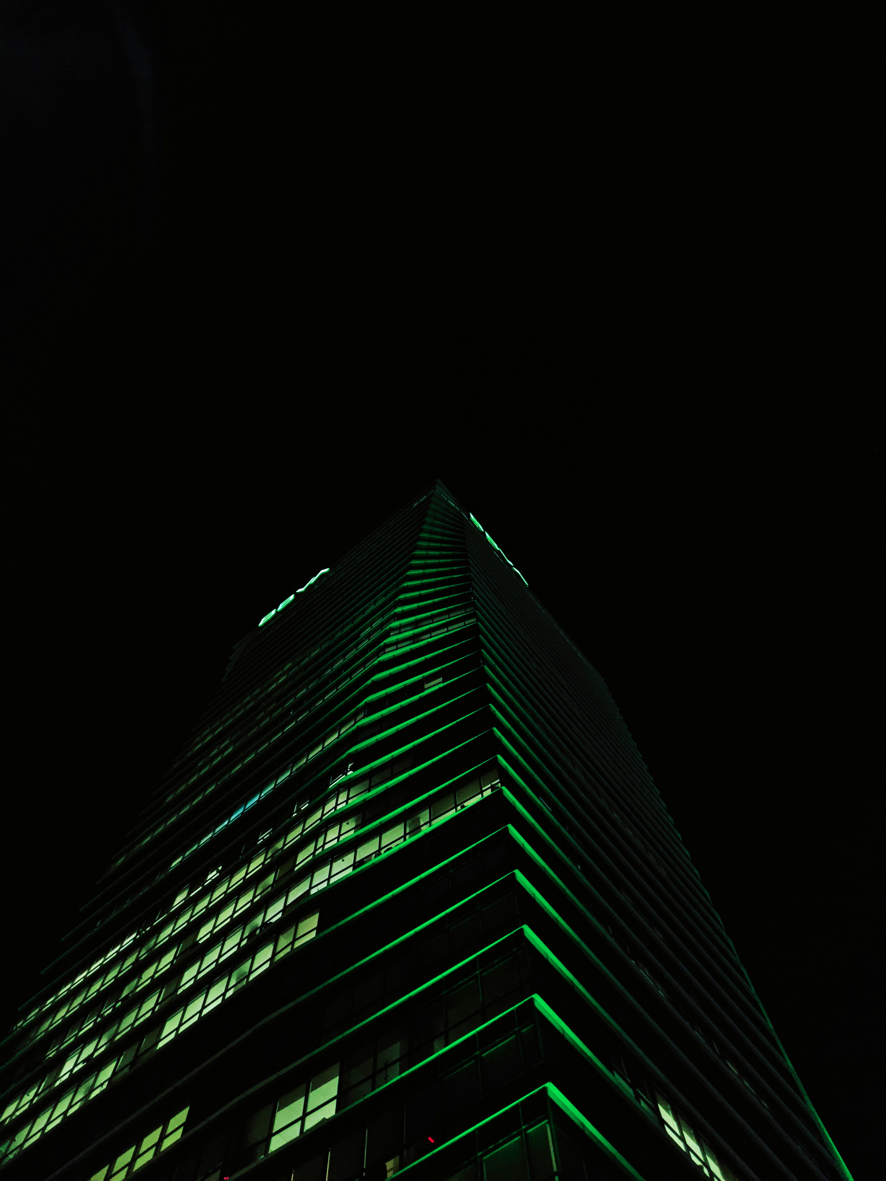 A sleek skyscraper illuminated by vibrant green lights against the night sky, showcasing modern architectural lines.