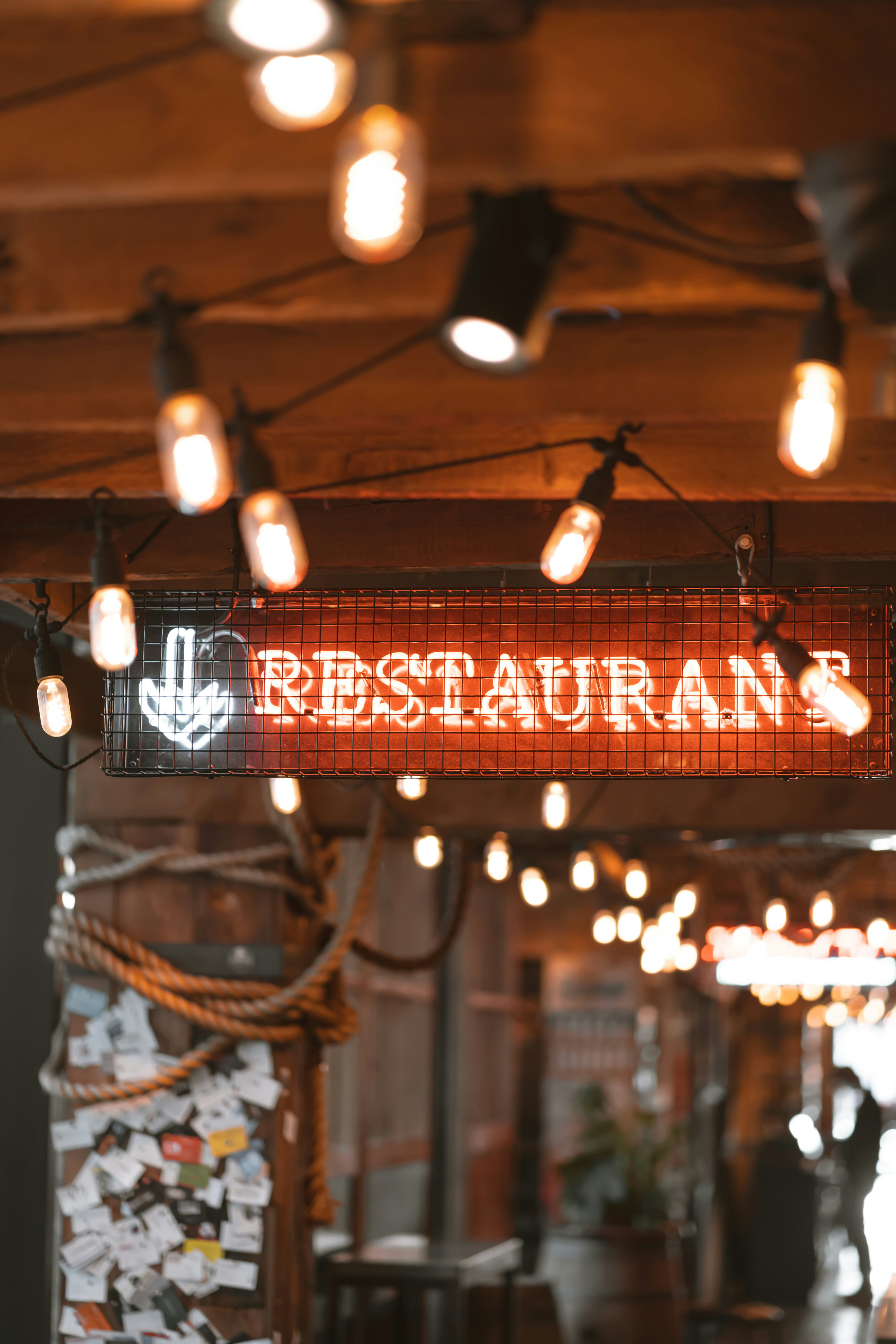 Neon 'RESTAURANT' sign surrounded by warm glowing bulbs in a rustic setting, guiding patrons towards dining experiences.