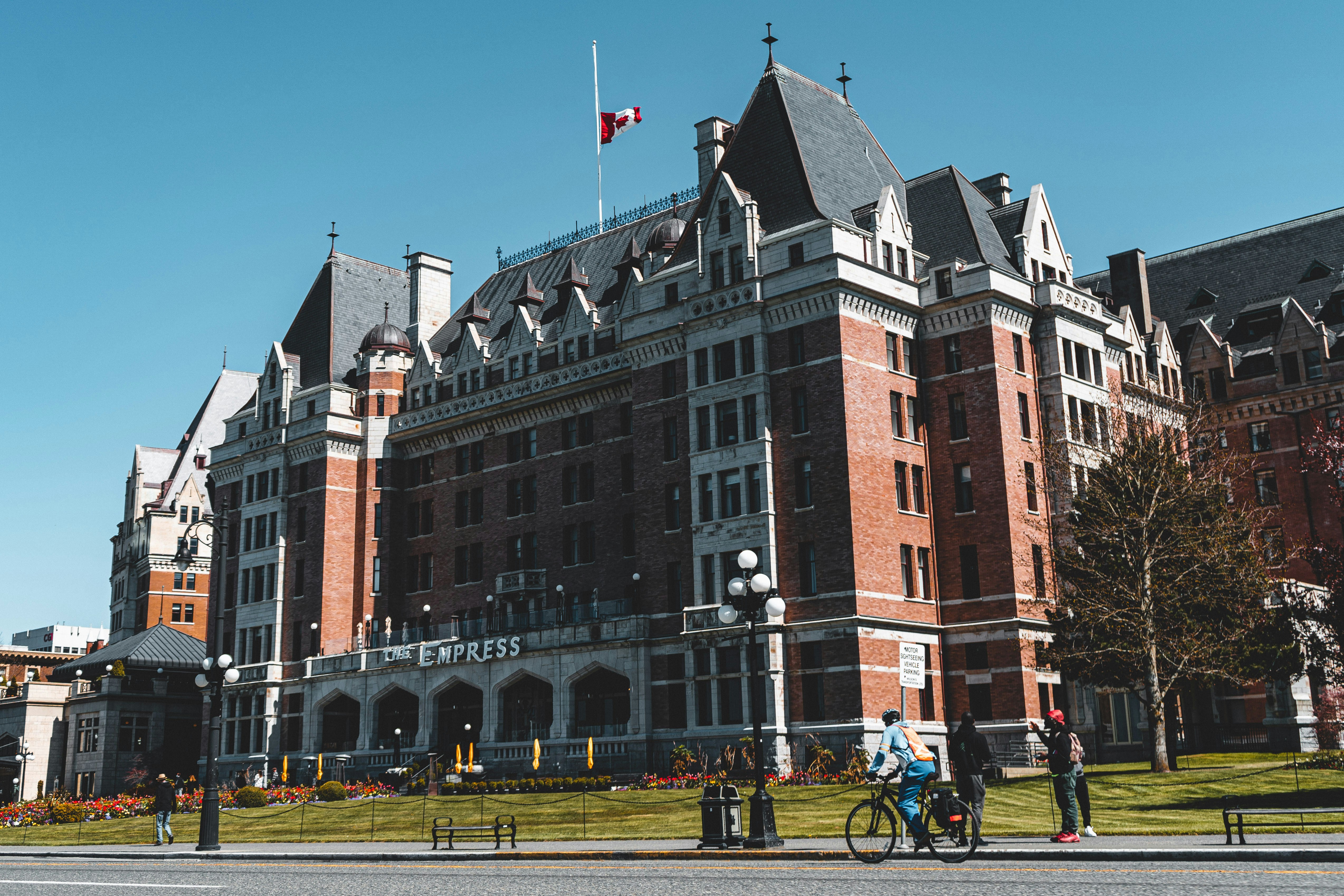 Historic Empress Hotel in Victoria, Canada, showcasing its intricate architecture and vibrant surroundings. A cyclist passes by, adding a dynamic element to the scene.