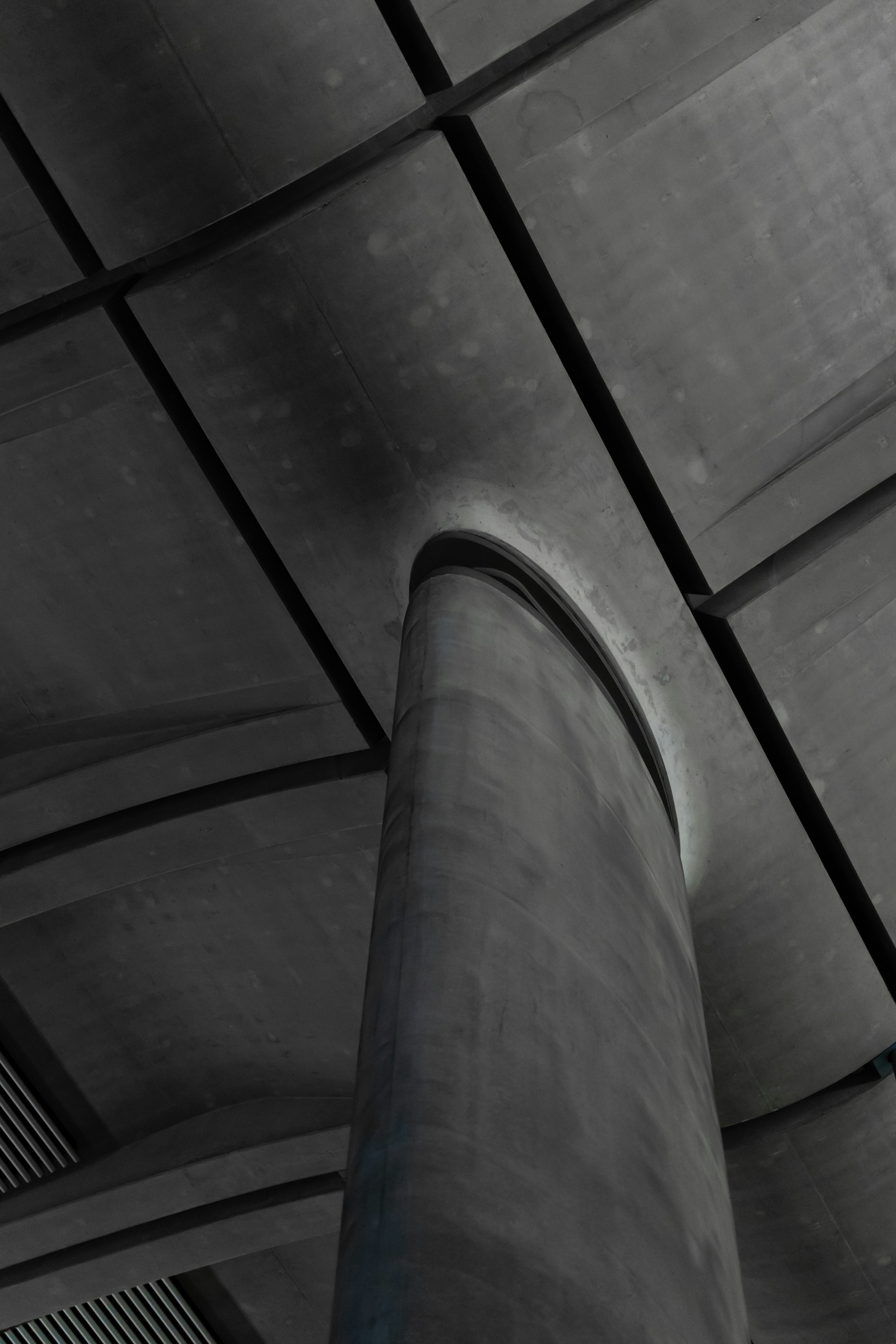 Abstract view of a large concrete column beneath a modern architectural structure, showcasing the interplay of lines and shadows.