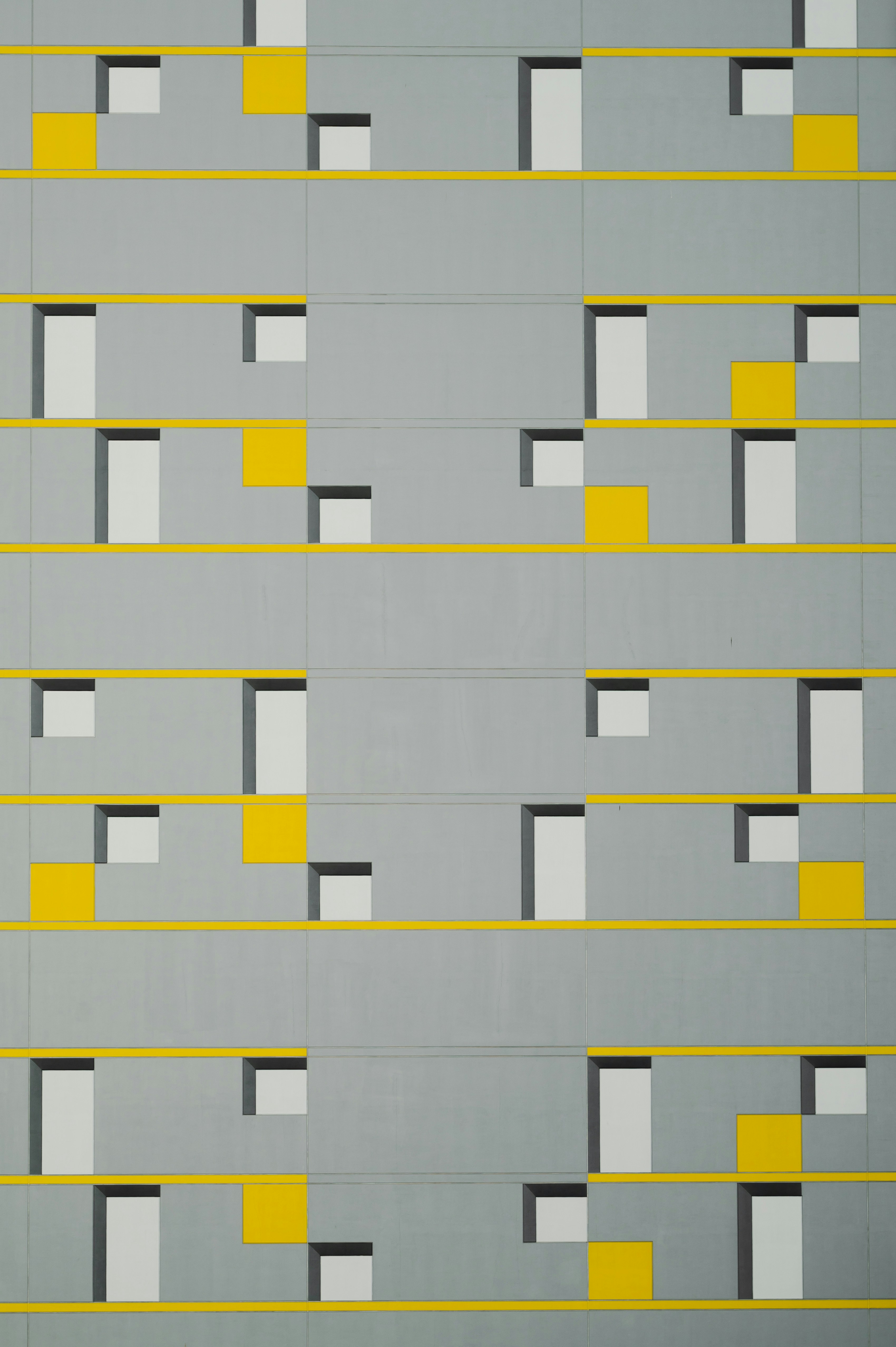 A contemporary building facade showcasing a pattern of gray, white, and yellow rectangles and squares, creating a visually striking geometric design.