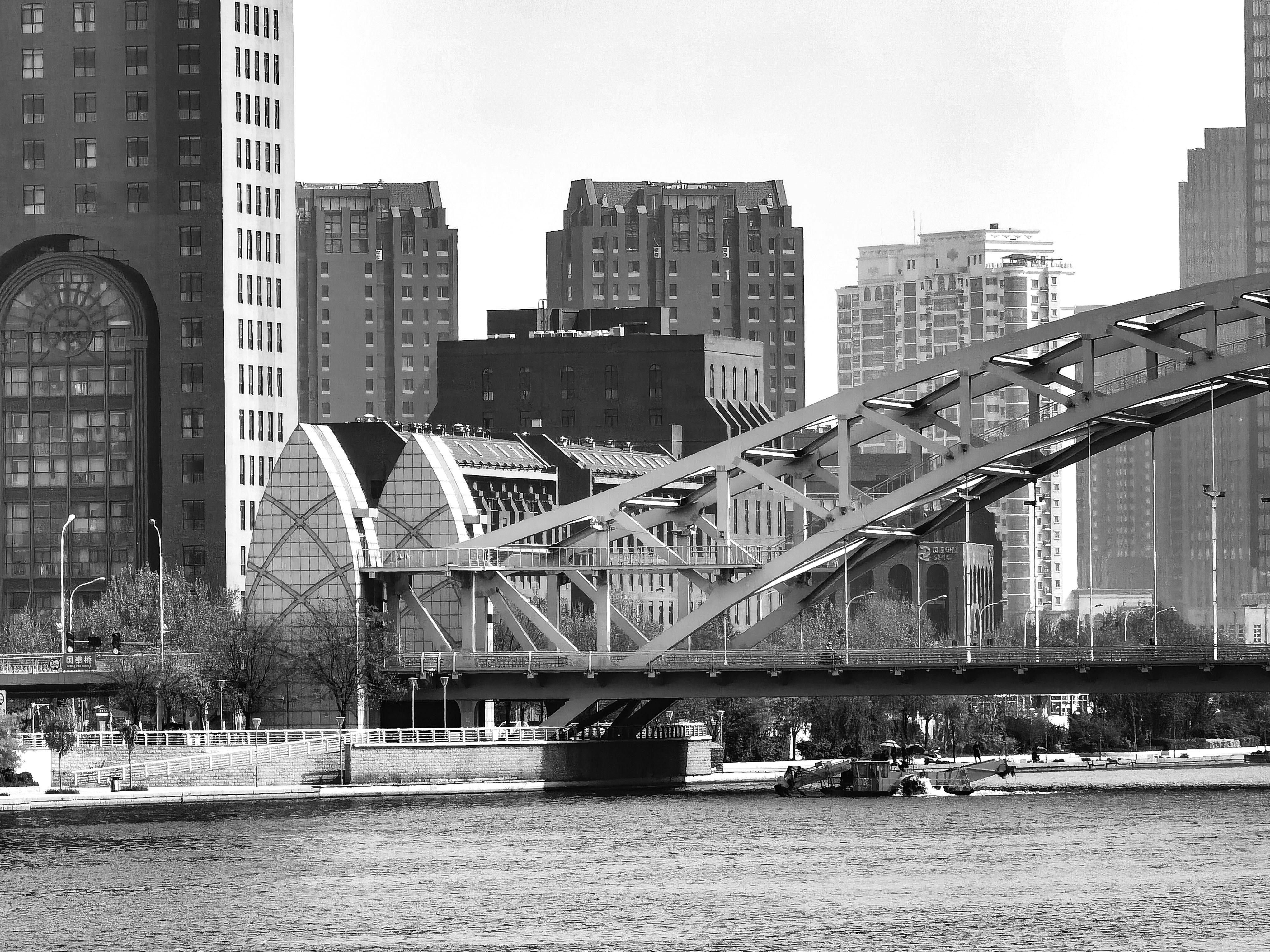 A modern bridge intersects with striking architectural forms in a bustling urban landscape, showcasing a blend of steel and glass structures along the waterfront.