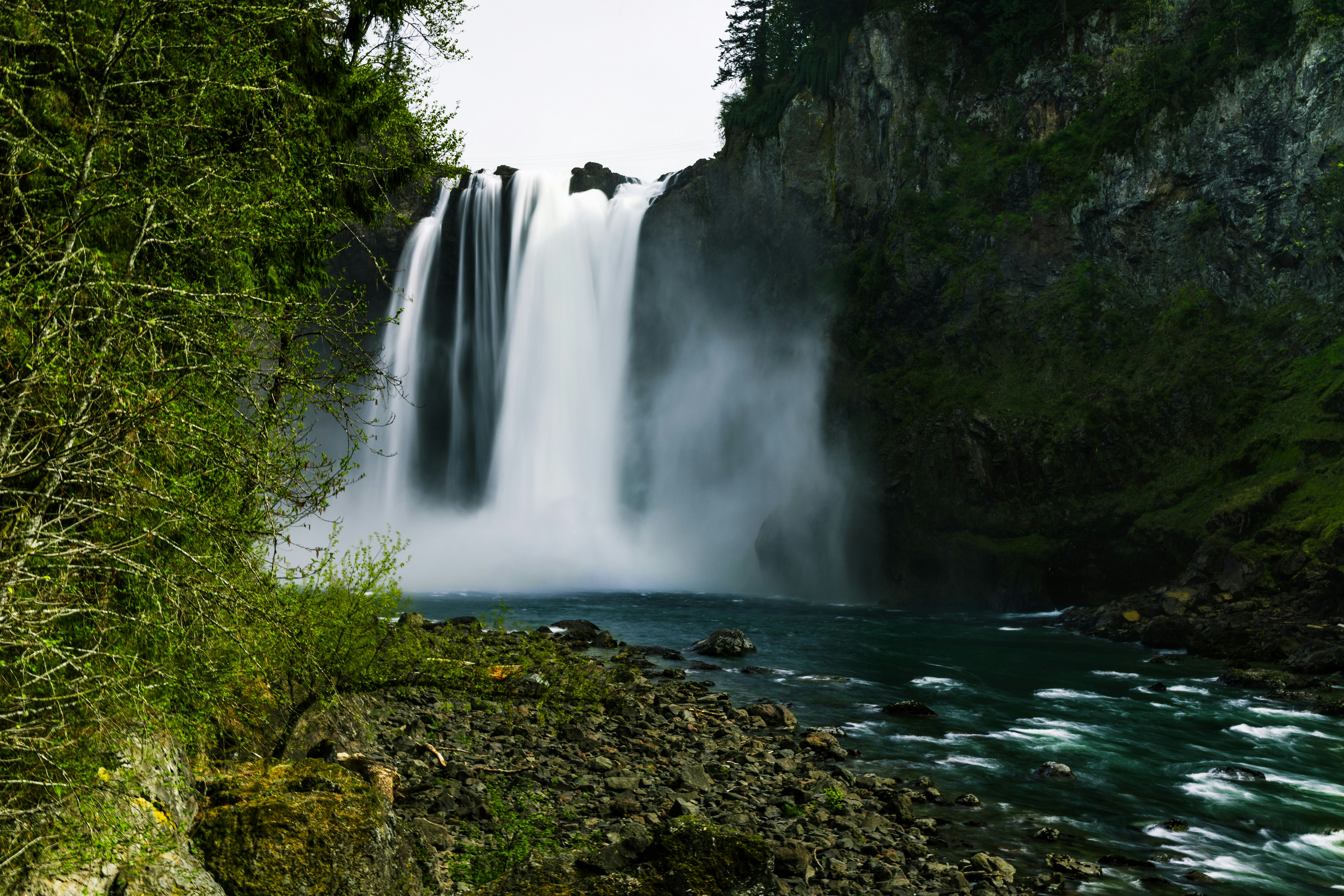 Majestic waterfall cascading down rocky cliffs, surrounded by lush greenery and a tranquil river below.