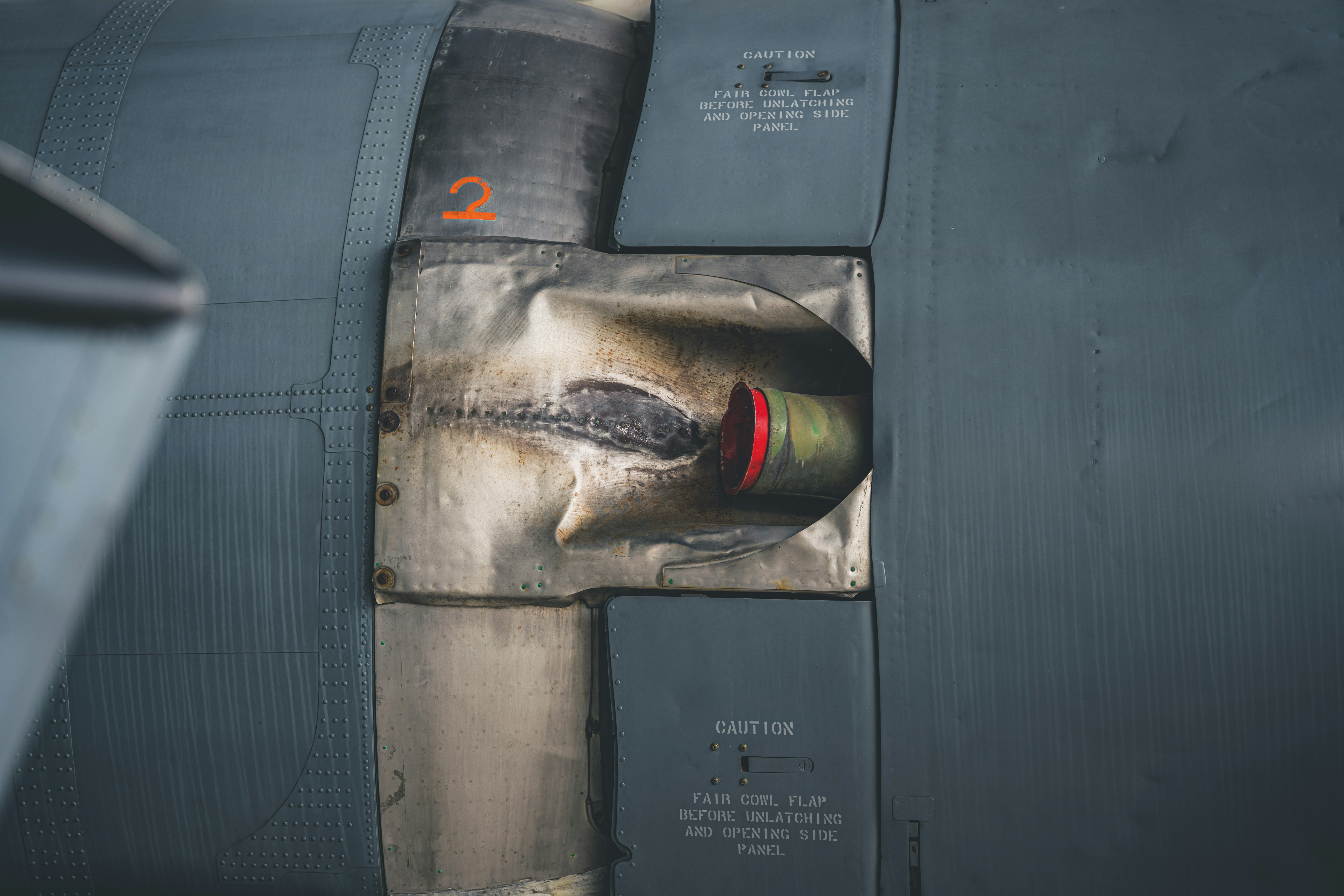 Red Vent Cap Peeks Through a Weathered Aircraft Nacelle Panel