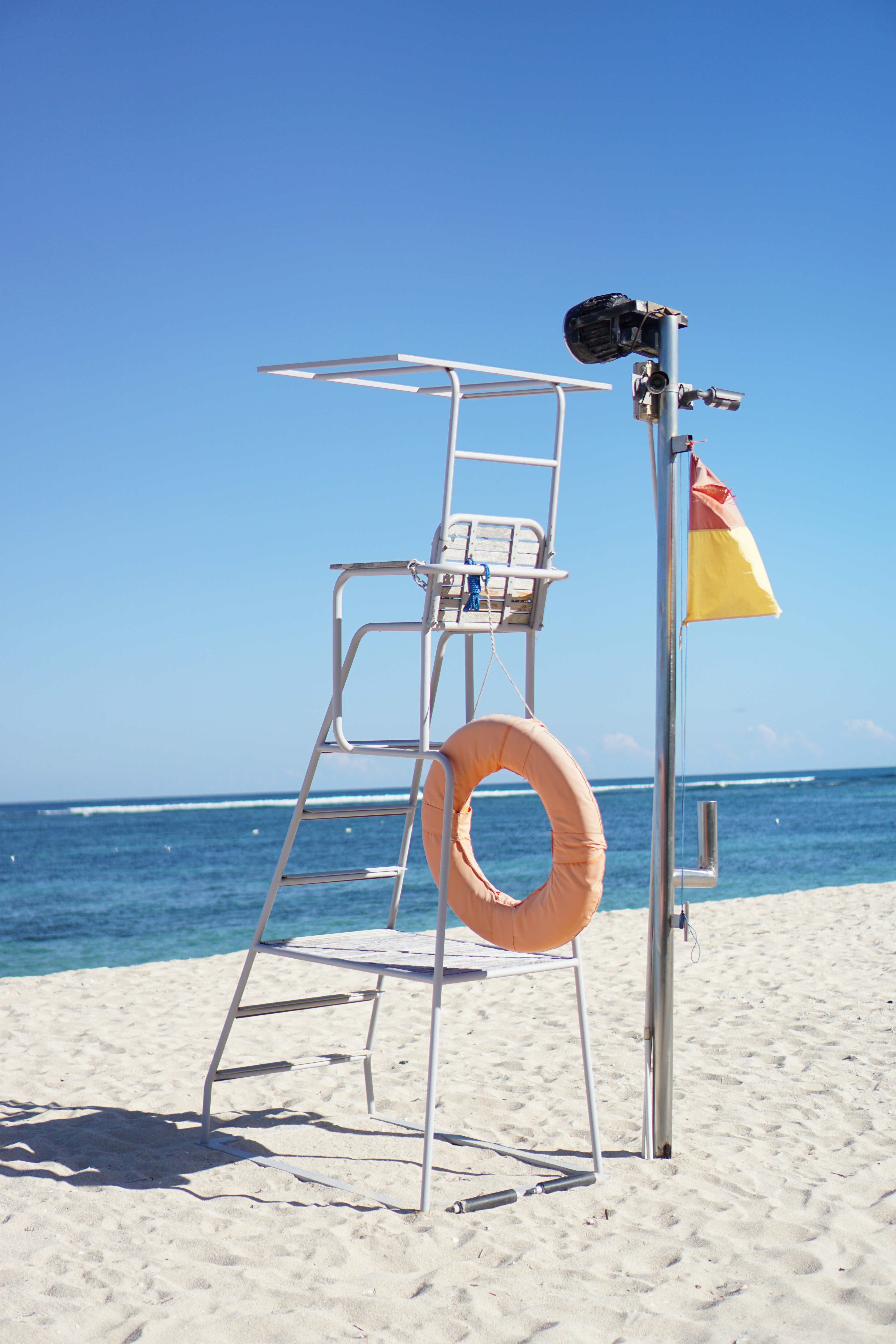 Lifeguard stand with an orange flotation ring and a safety flag overlooking a serene beach and calm ocean waves.