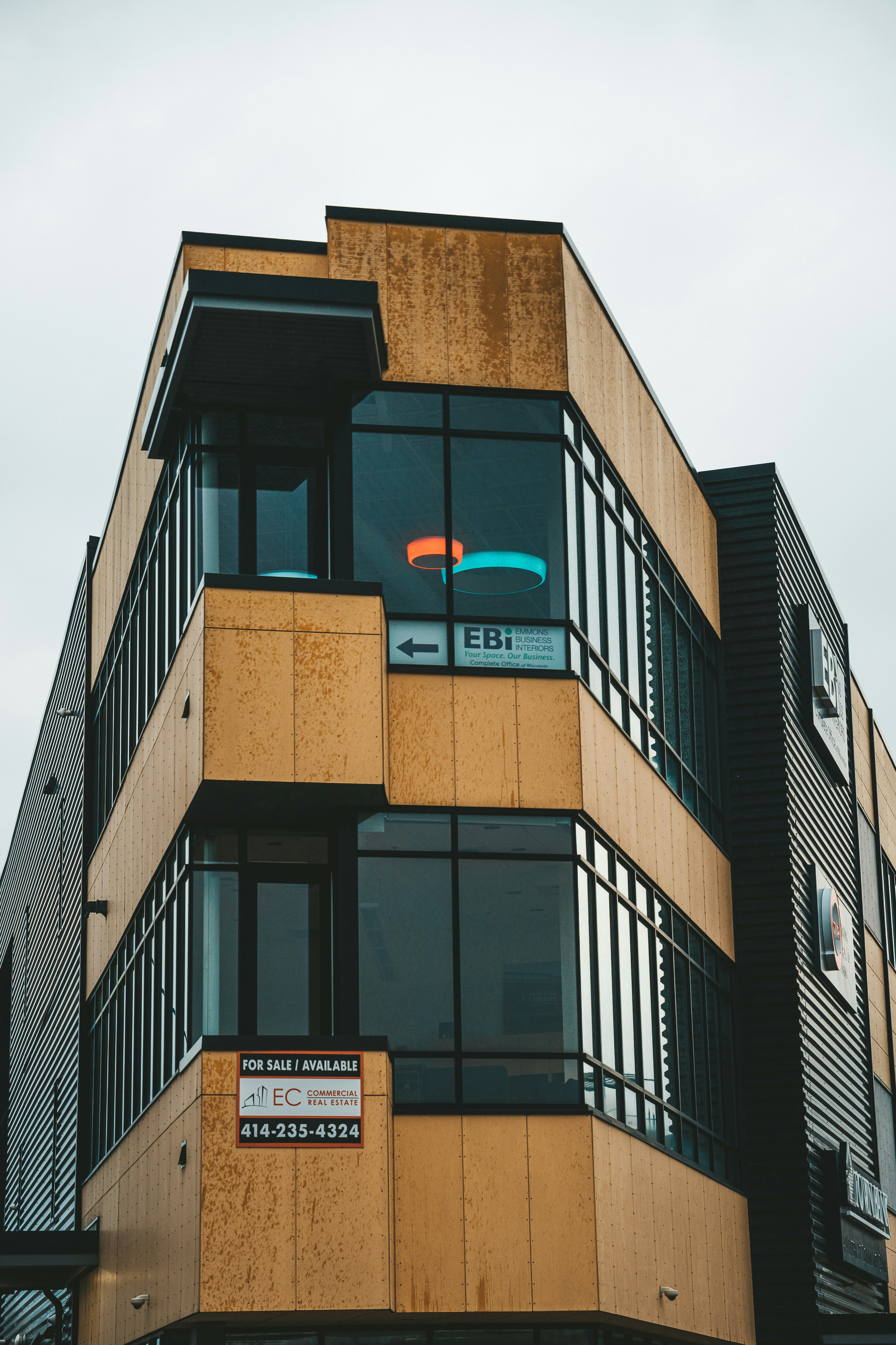 Contemporary building corner showcasing large windows and vibrant interior lighting against a cloudy sky.