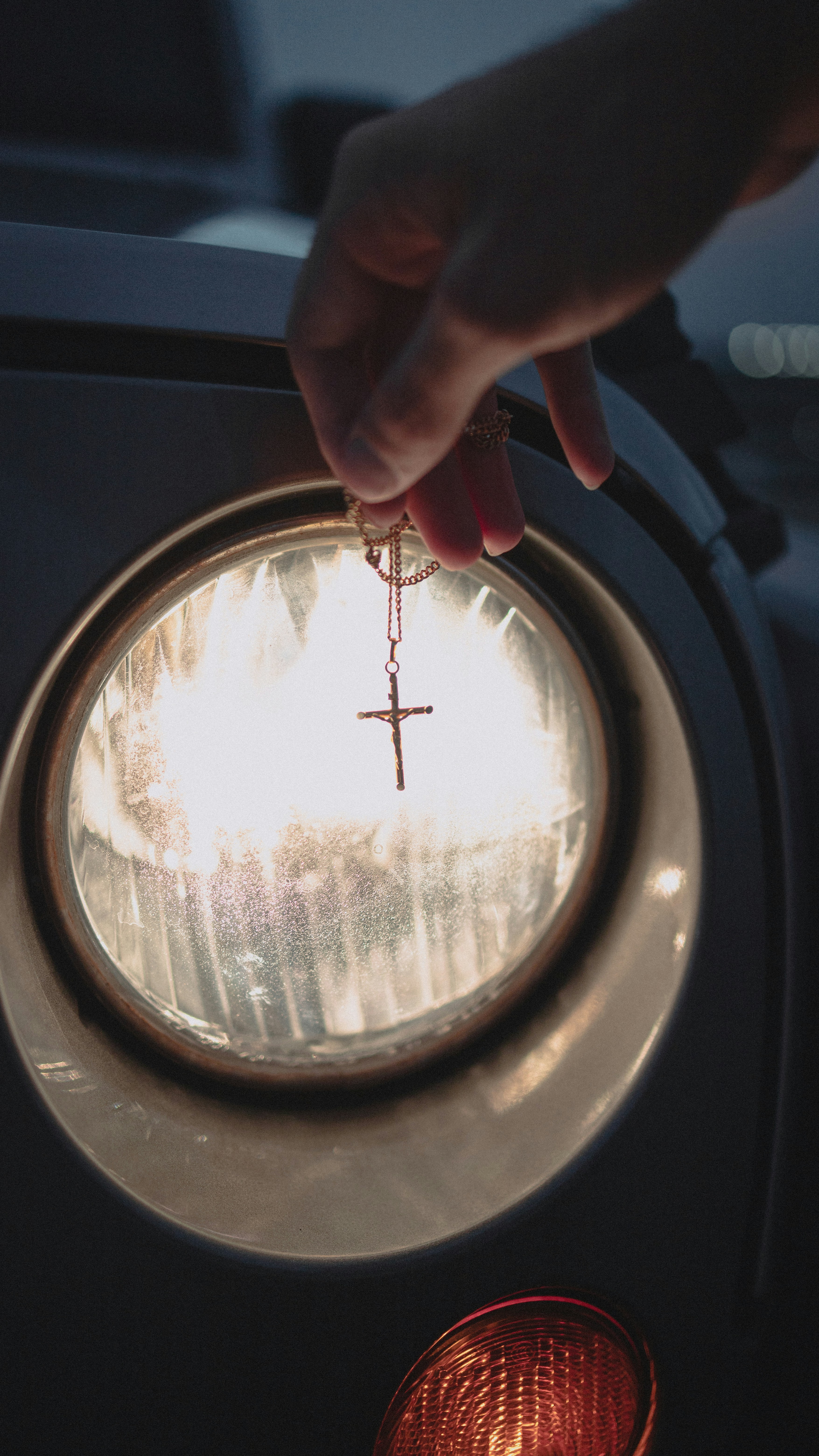 Cross Pendant Hovering Over a Car Headlight at Dusk