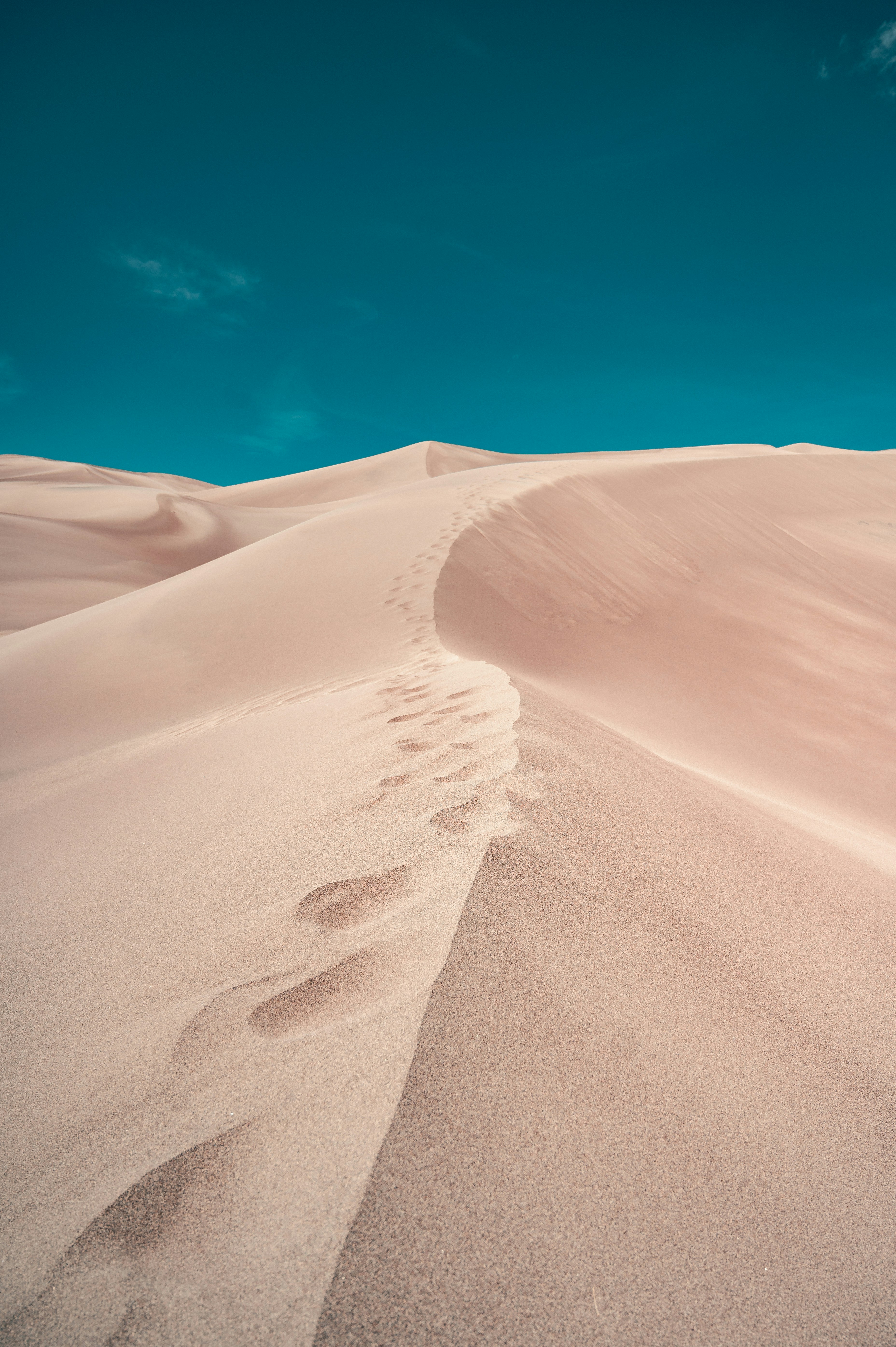 Footprints tracing a winding path across soft, golden sand dunes under a vivid sky.