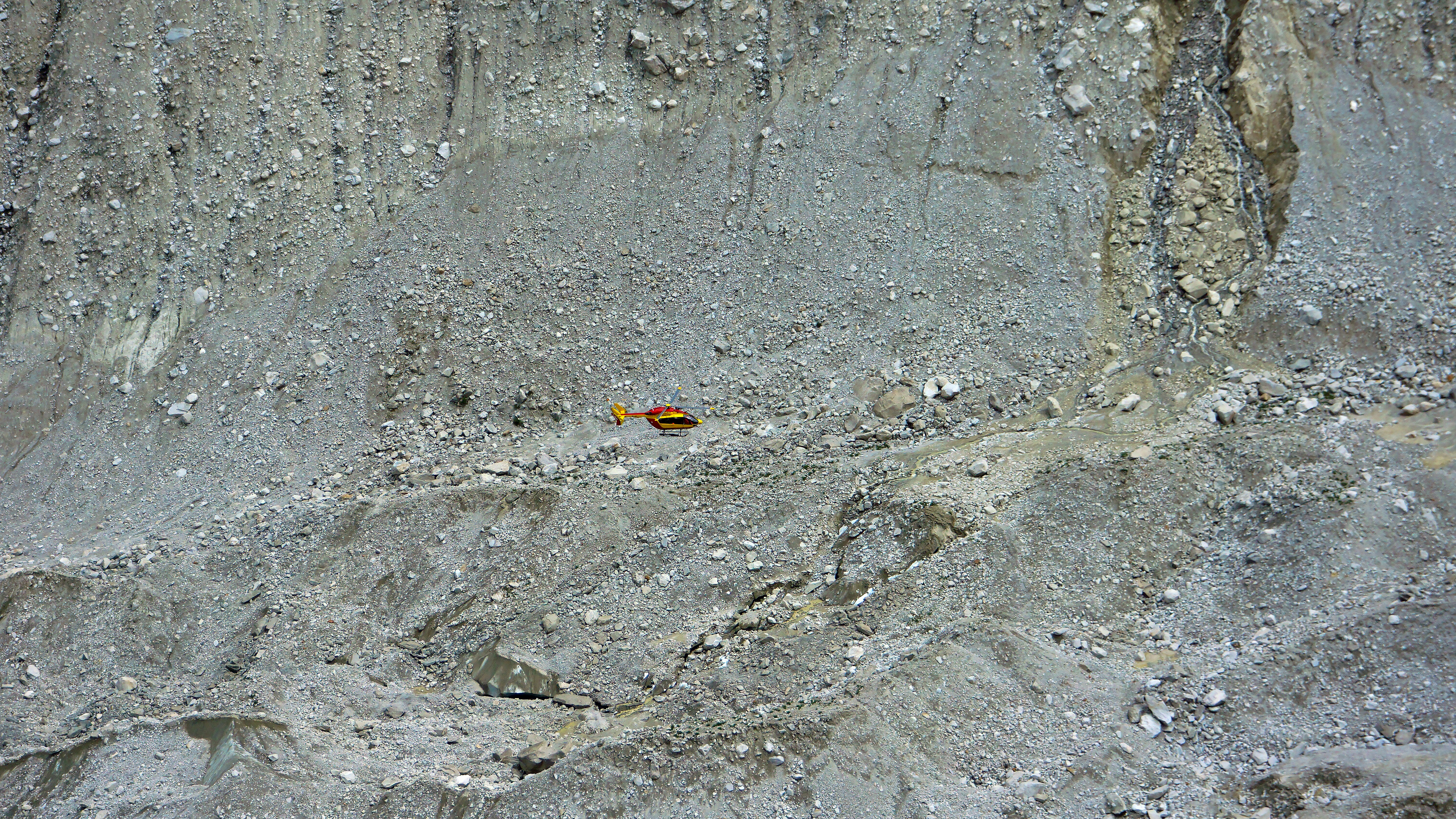 A bright yellow rescue helicopter positioned on a rocky, gray landscape, highlighting the challenges of aerial operations in rough environments.