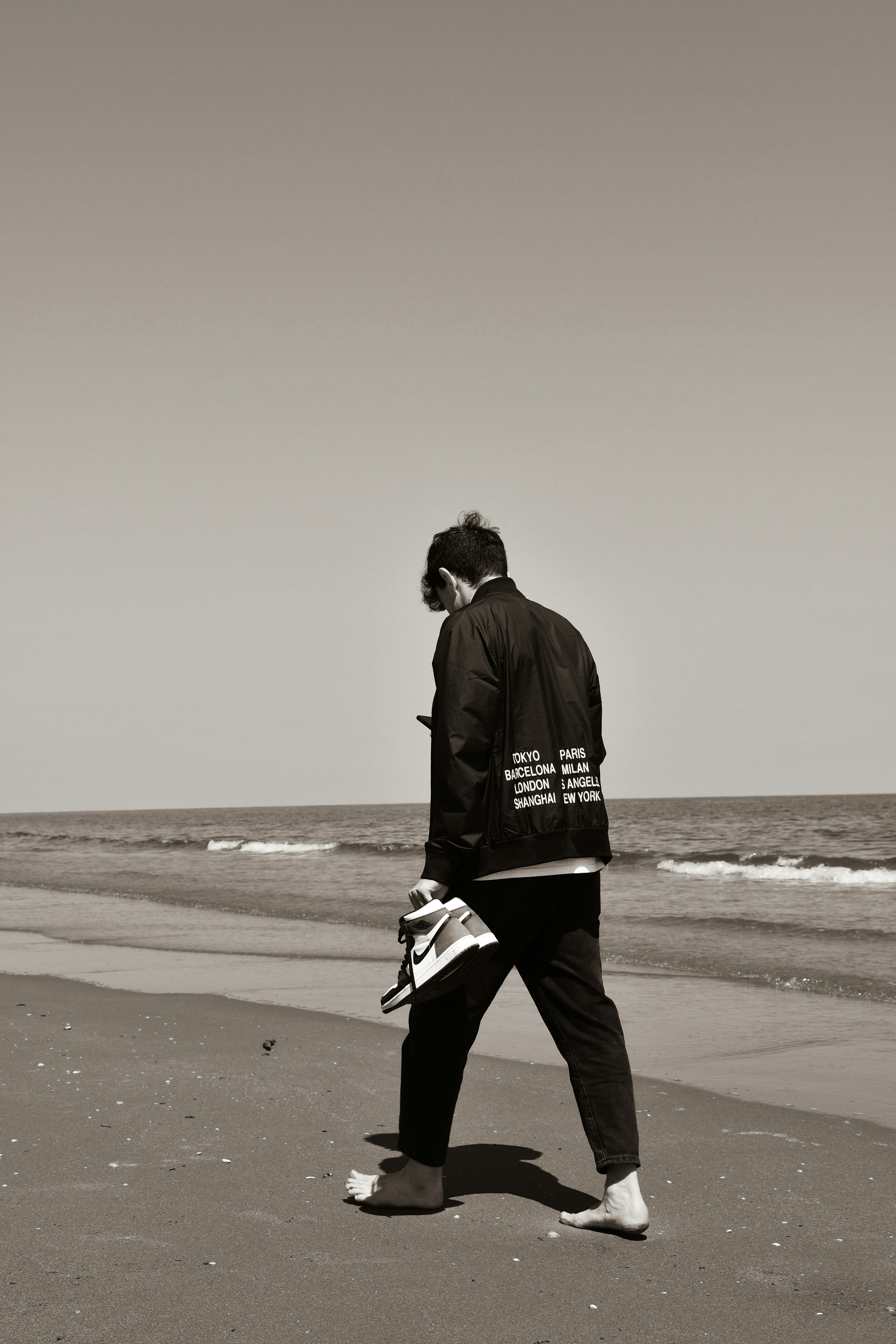 Silent silhouette: a lone man treads the shoreline with a folded jacket in hand