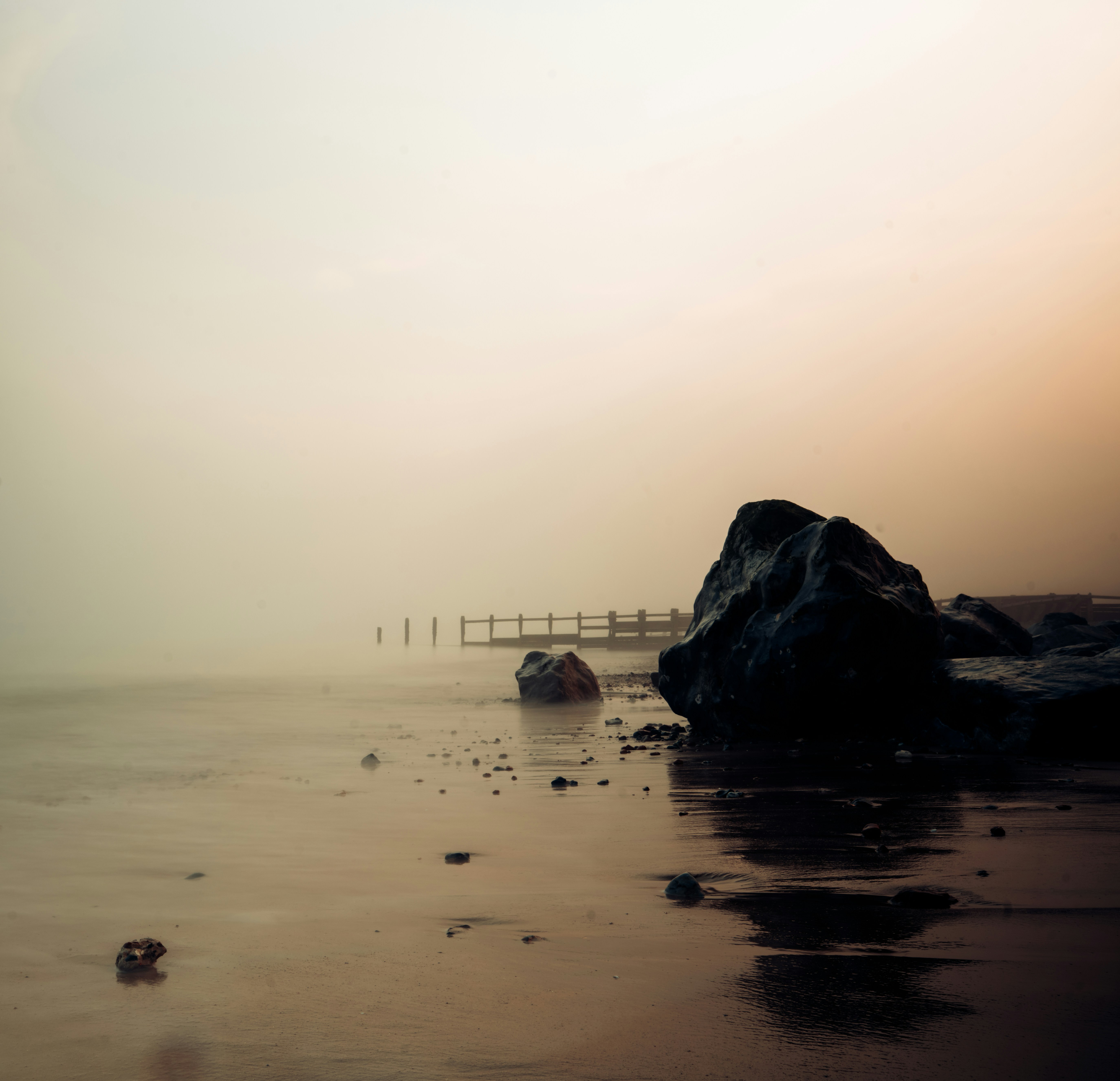 A foggy beach with rocks and a bridge in the distance photo – Free Uk ...