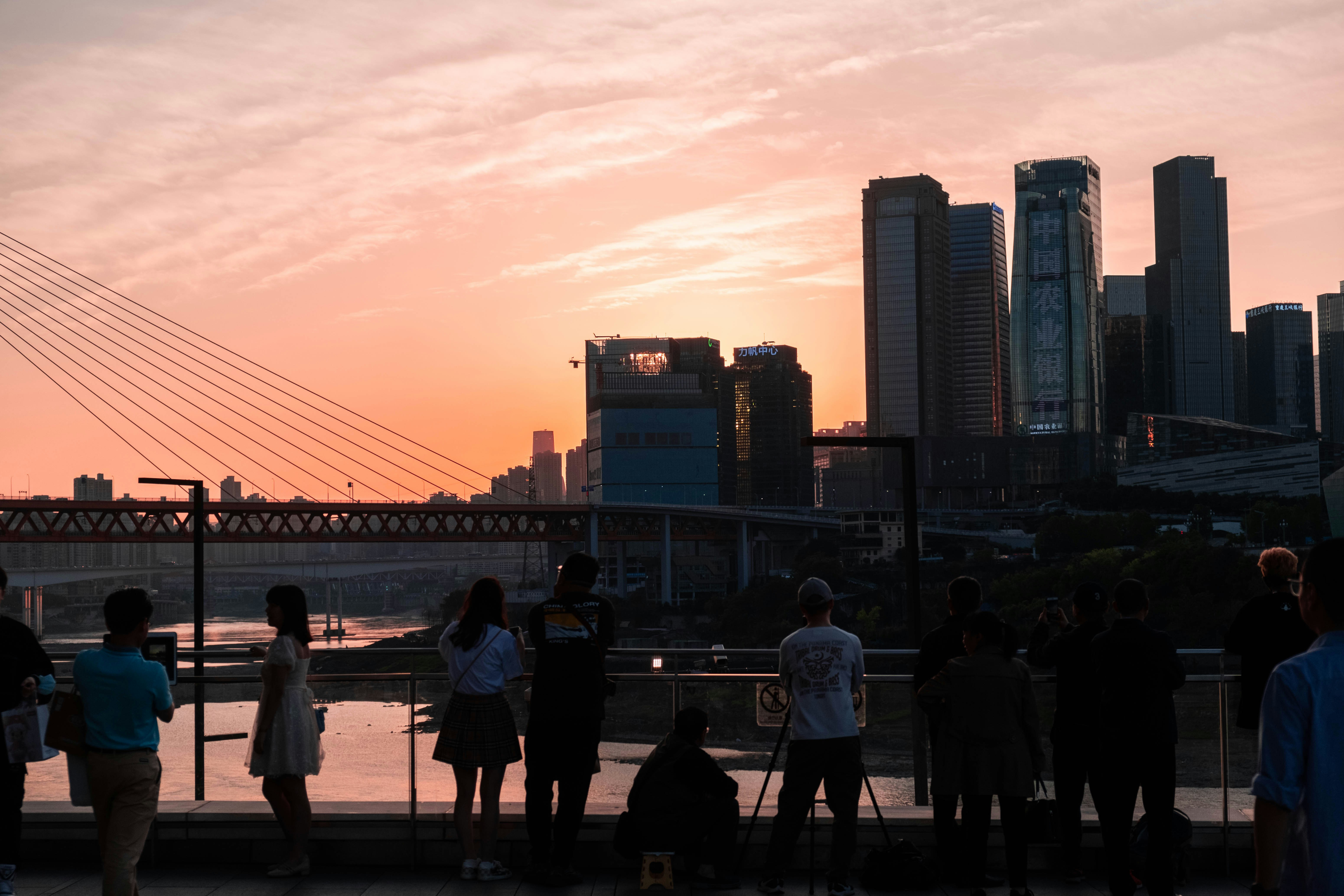 City Skyline at Sunset with Silhouetted Riverside Onlookers