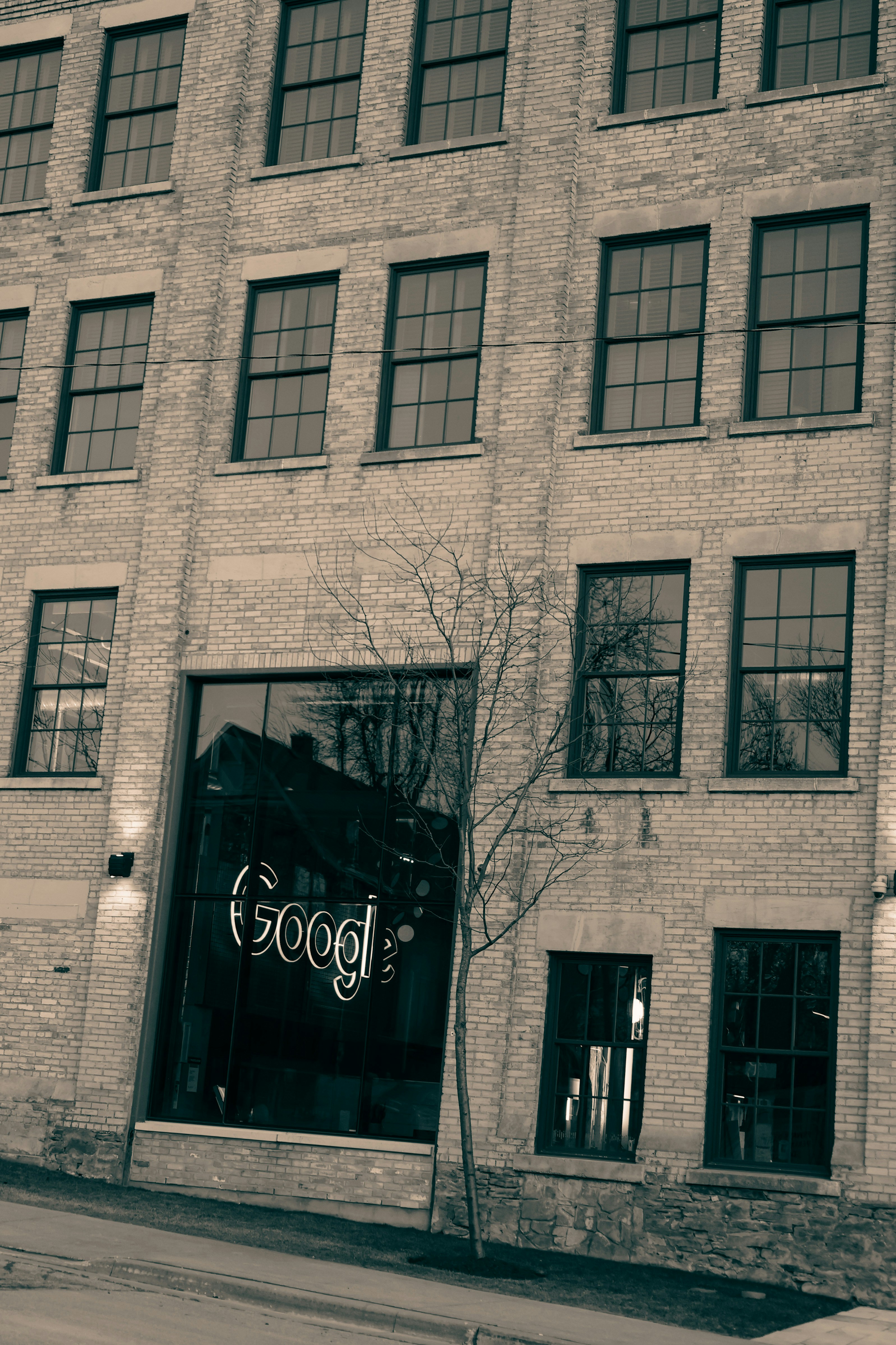 Grayscale photo of a brick building with a Google logo in a large window.