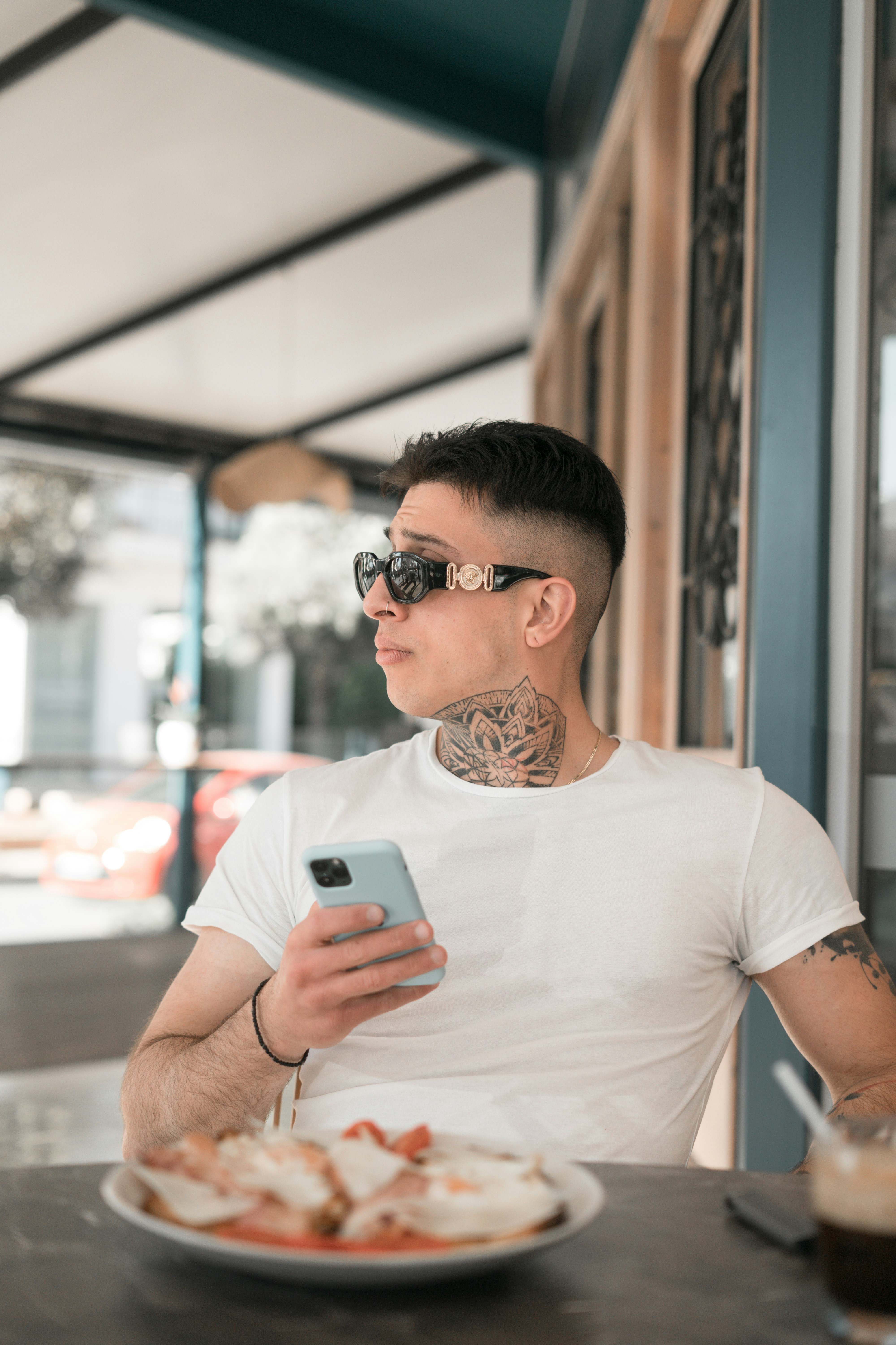 Sunlit Café Portrait: A Tattooed Man Checks His Phone