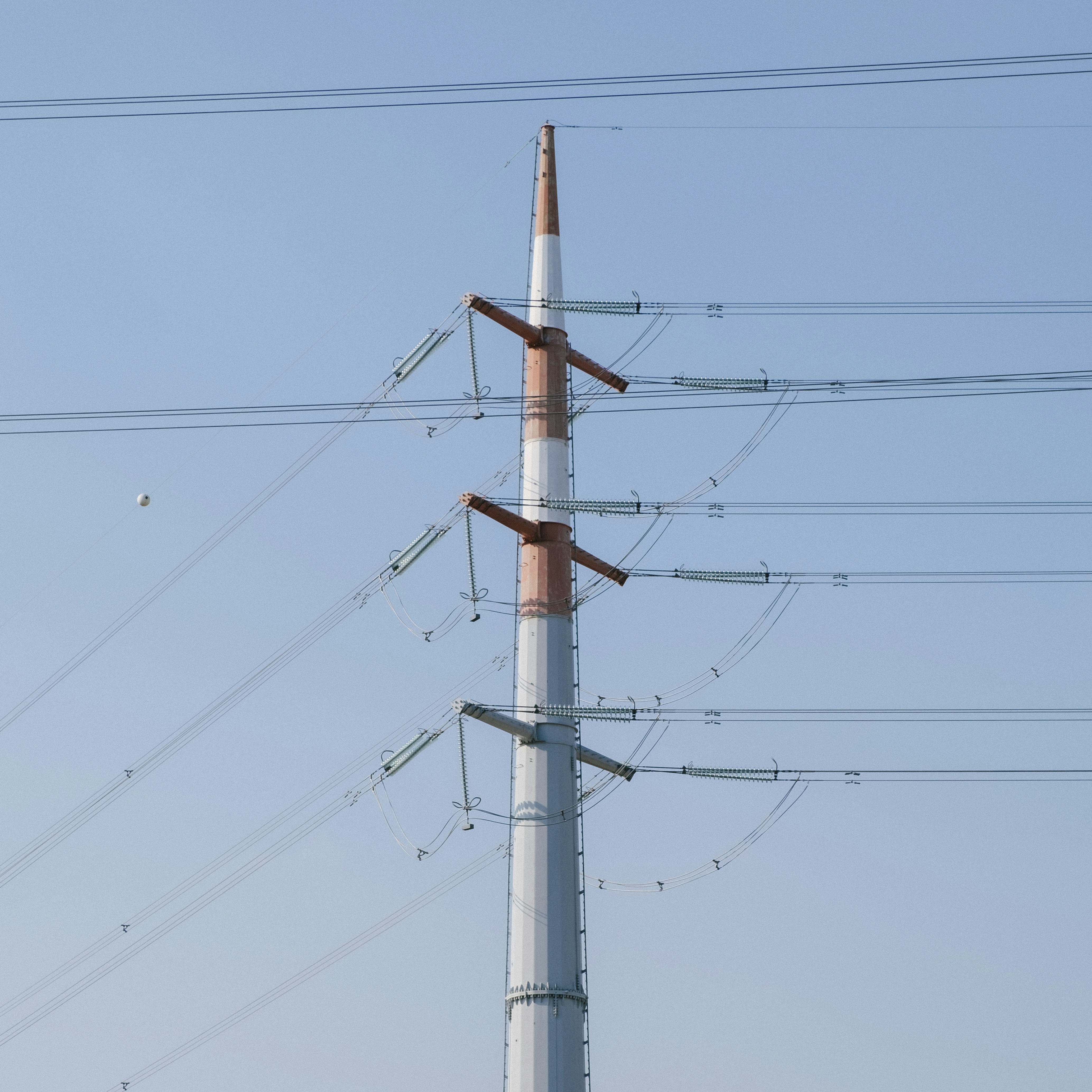 A tall power transmission tower stands against a clear blue sky, with power lines extending in various directions. The structure's design emphasizes its role in energy distribution.