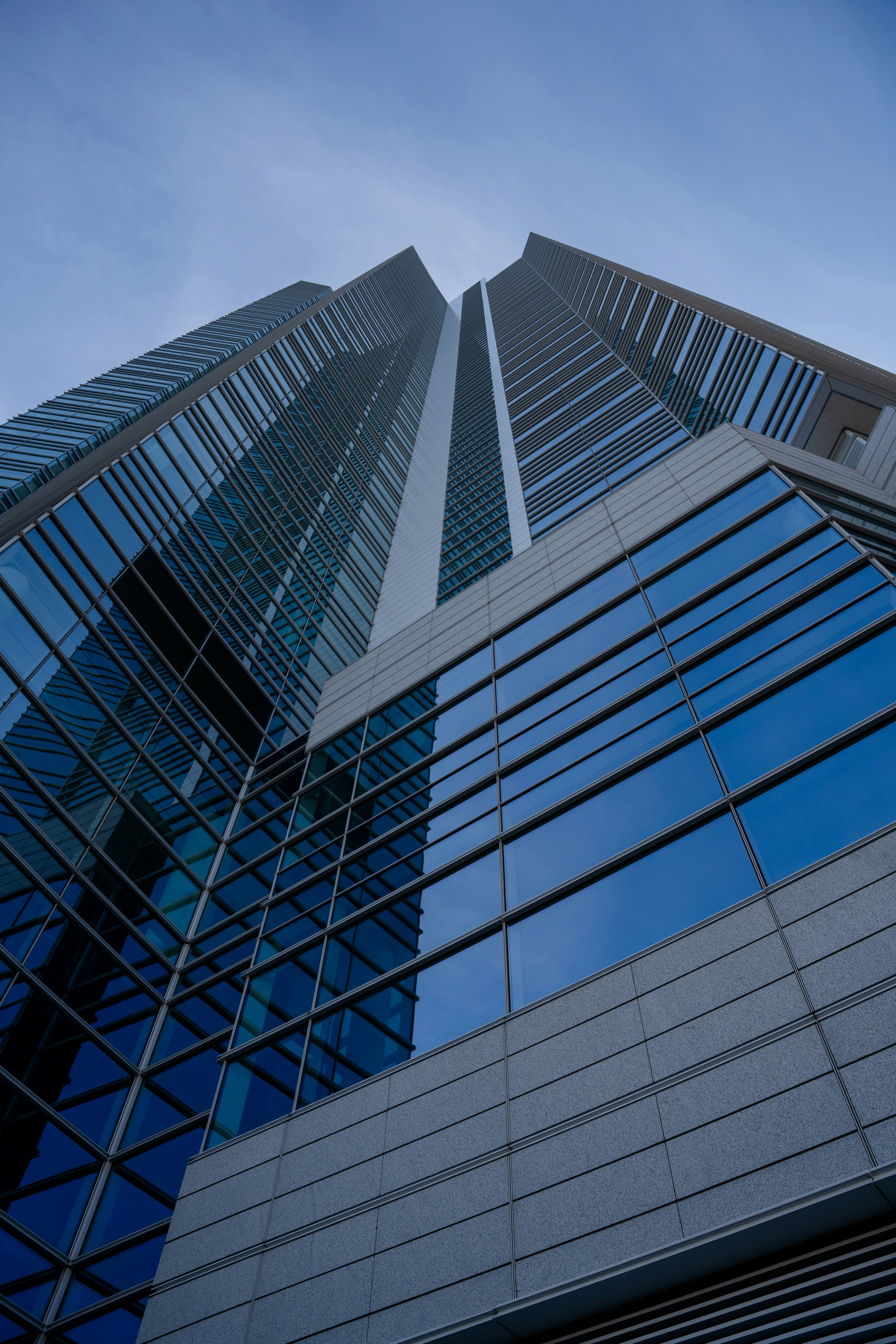 Skyscraper reflecting the sky and surrounding structures, captured from a low angle. The geometric lines and glass panels create a modern architectural marvel.