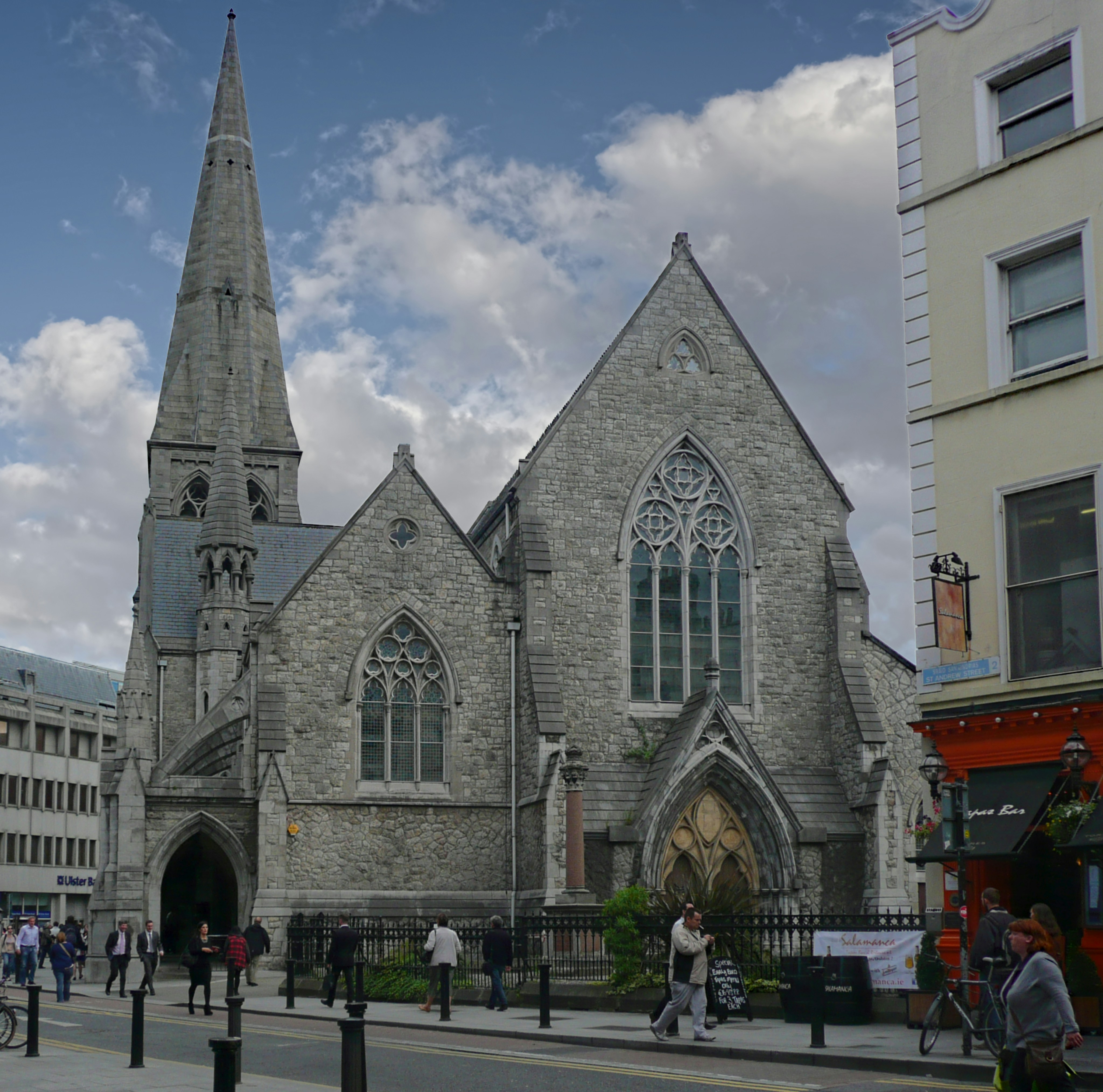 Historic stone church with intricate architecture stands amidst modern city life, showcasing a blend of past and present.
