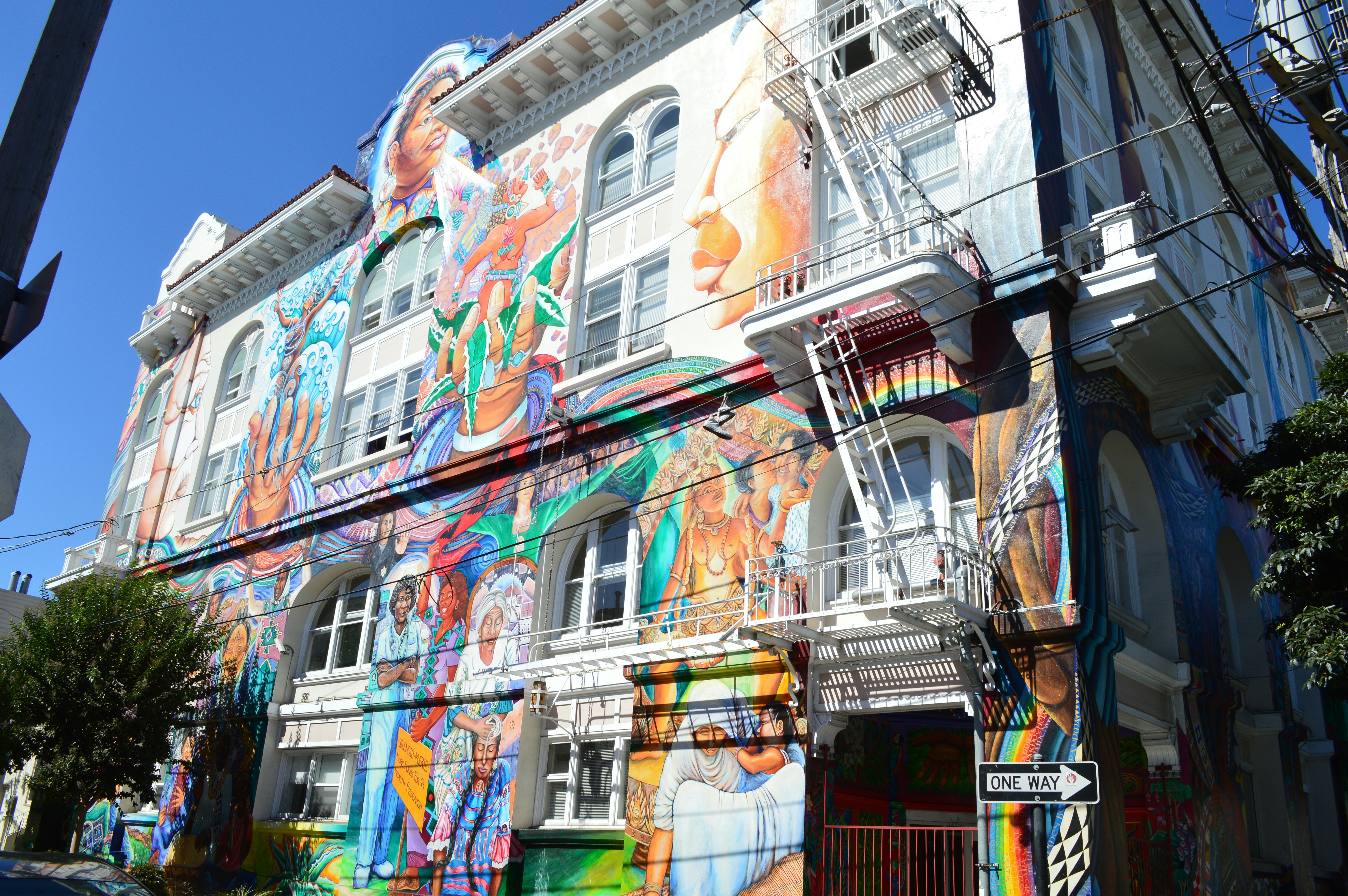Colorful mural covering a multi-story building under a clear blue sky.