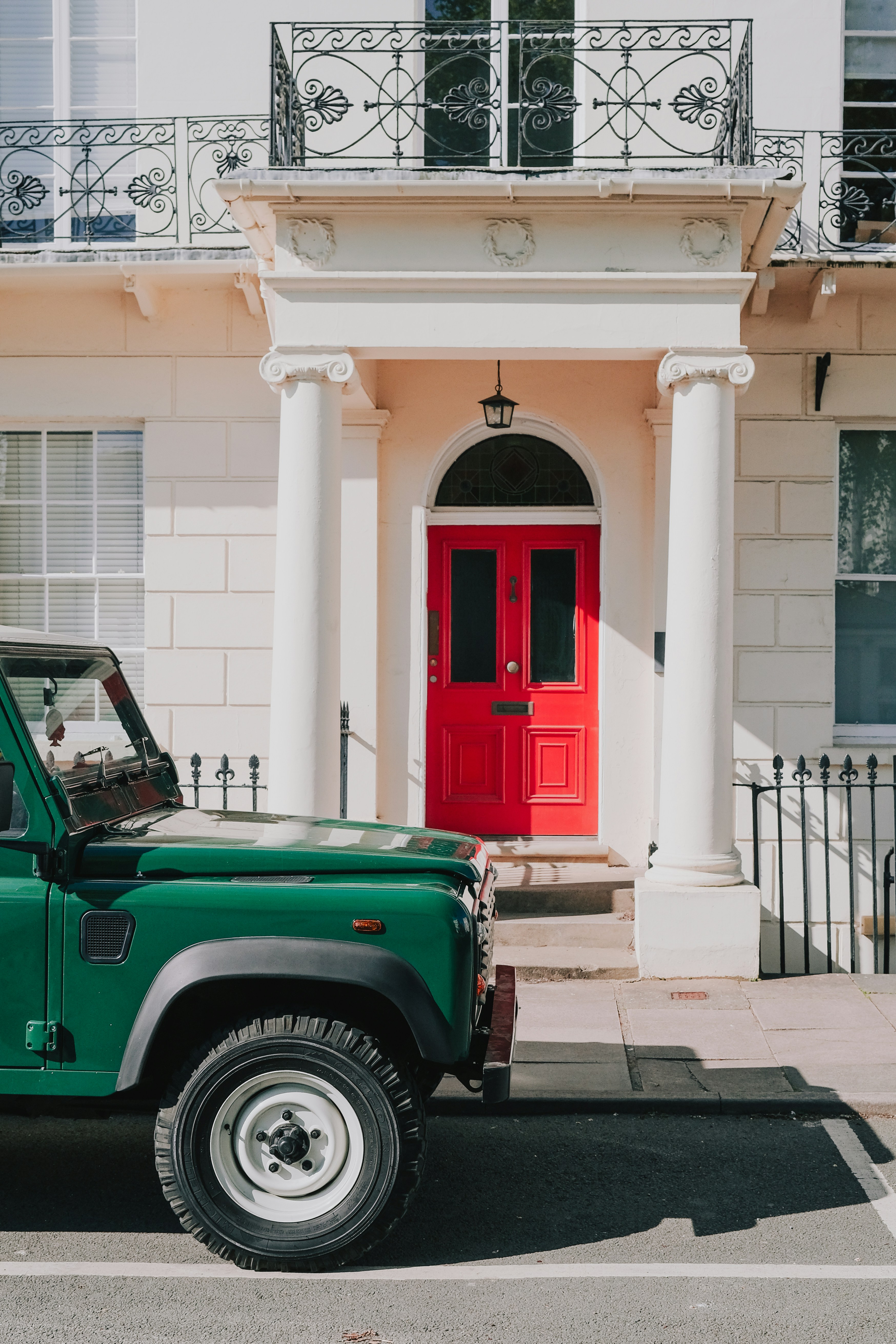 Crimson Front Door Under Neoclassical Columns, Framed by a Green Jeep