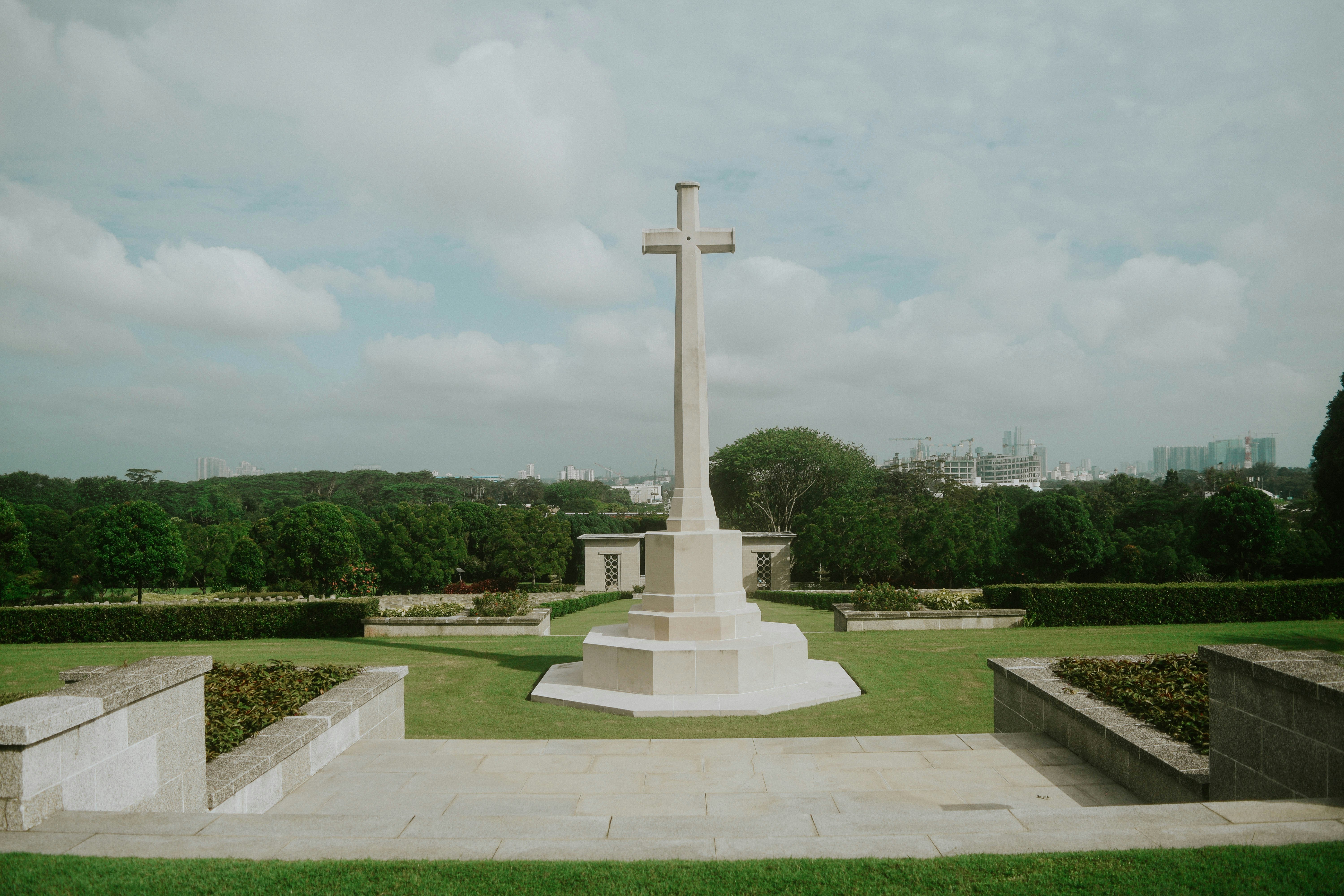 White concrete cross statue on green grass field under white clouds ...