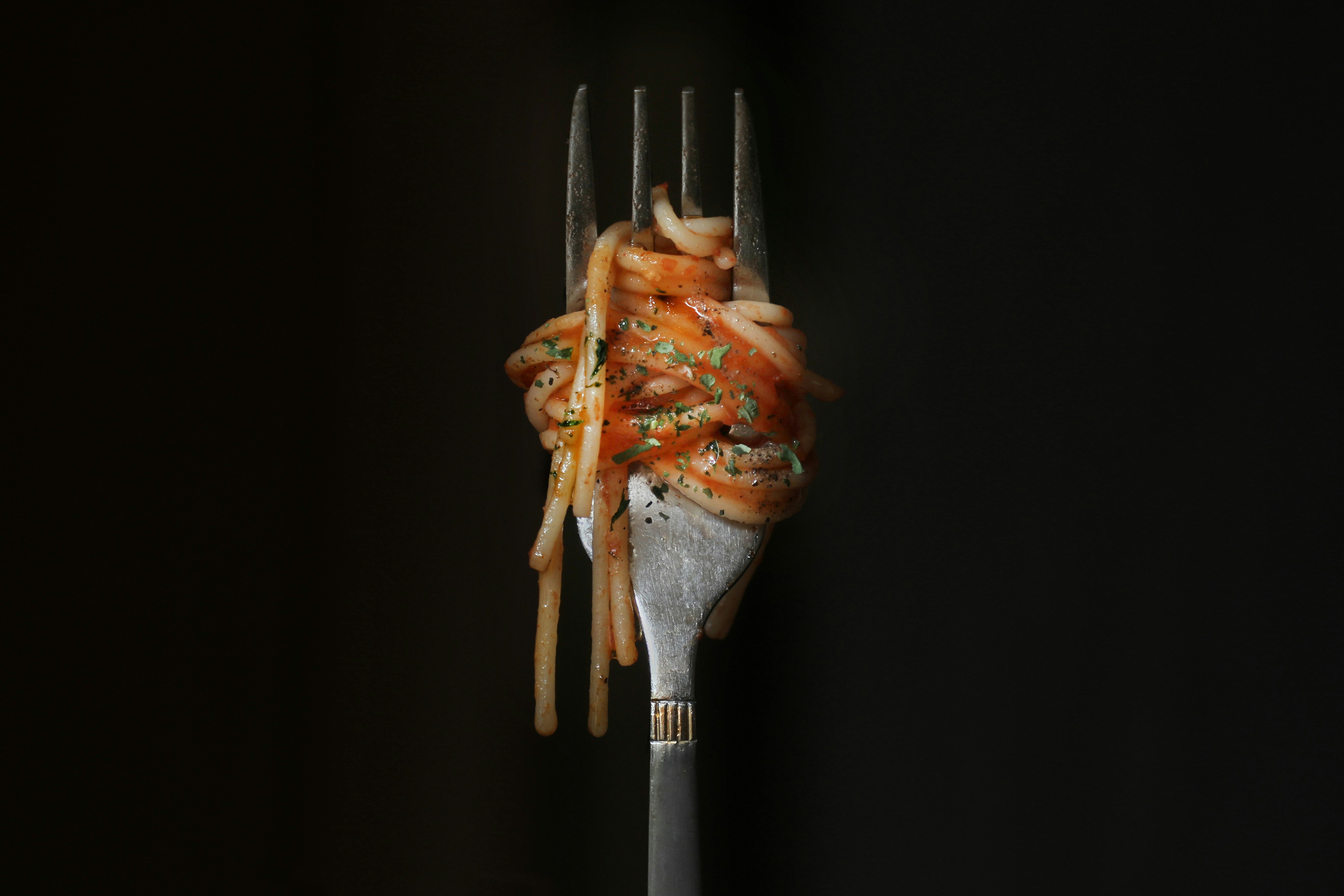 Spaghetti artfully twirled around a fork, garnished with herbs against a dark backdrop.