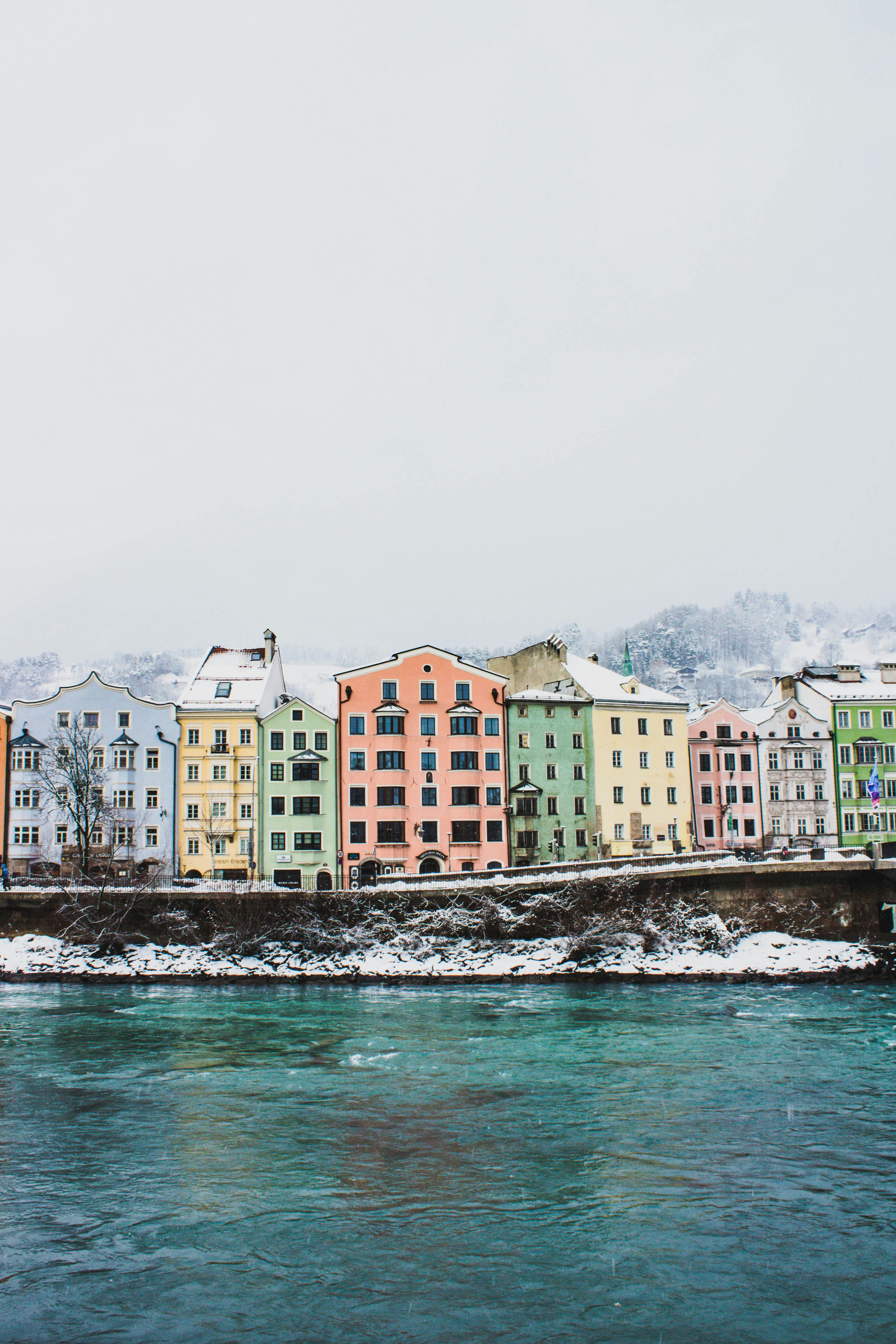 Colorful buildings lining a snow-dusted riverbank, reflecting the serene winter atmosphere. The scene captures a harmonious blend of architecture and nature.