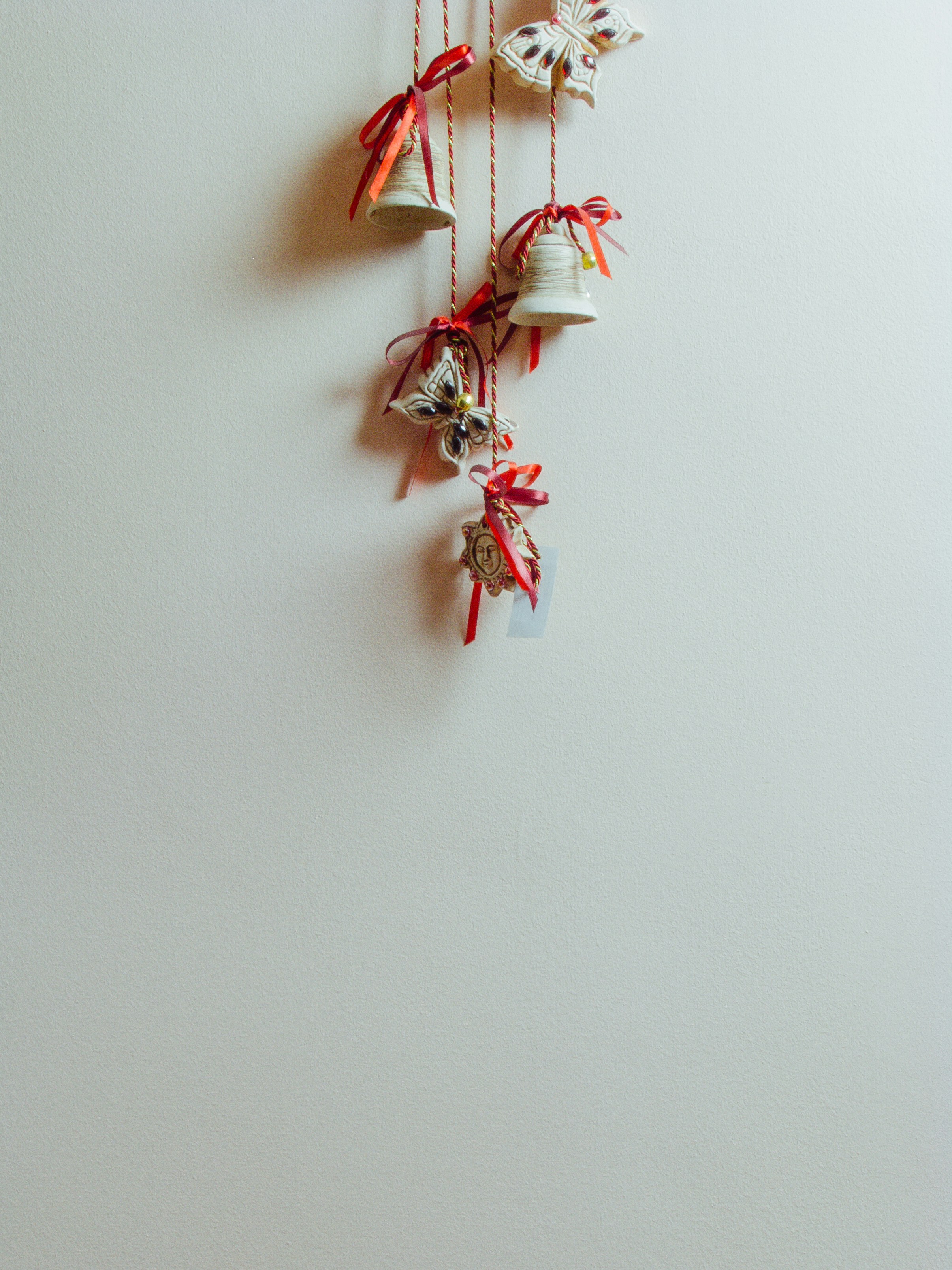 Delicate decorative bells with red ribbons hanging against a neutral wall, embodying a festive spirit.